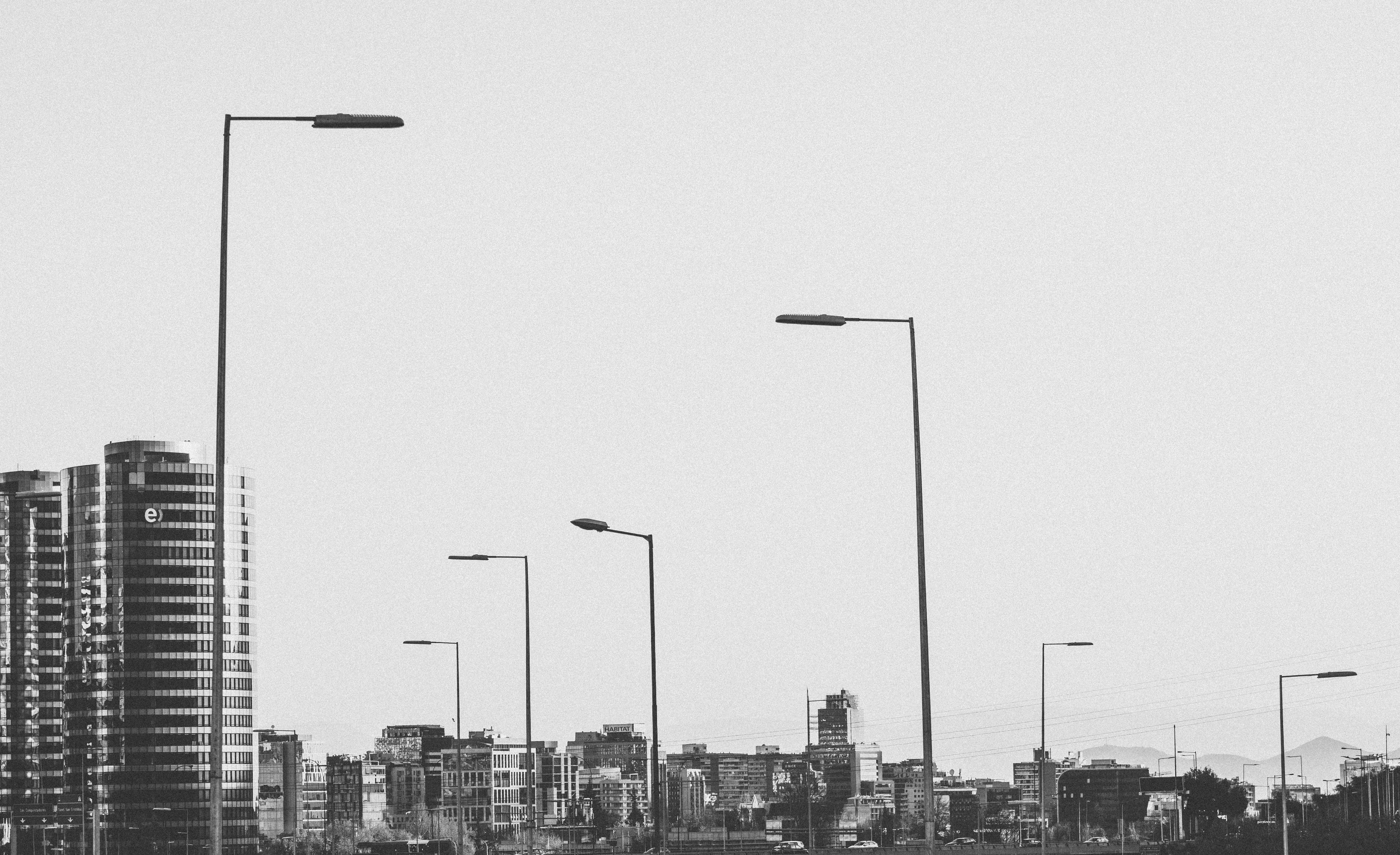 Black and white cityscape with tall streetlights and distant buildings under a clear sky.