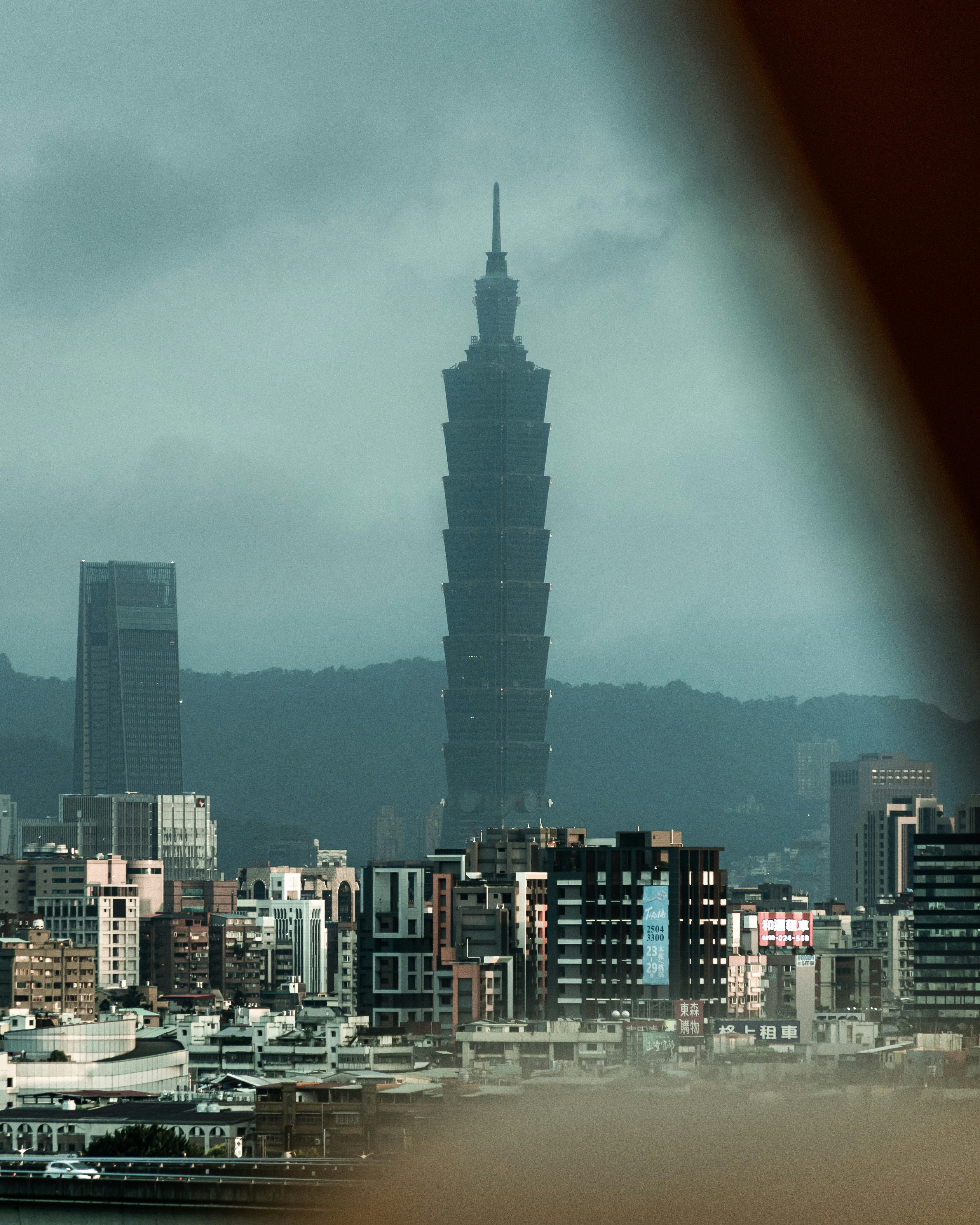 Taipei 101 Through a Window Frame: A Misty Cityscape Against Distant Hills