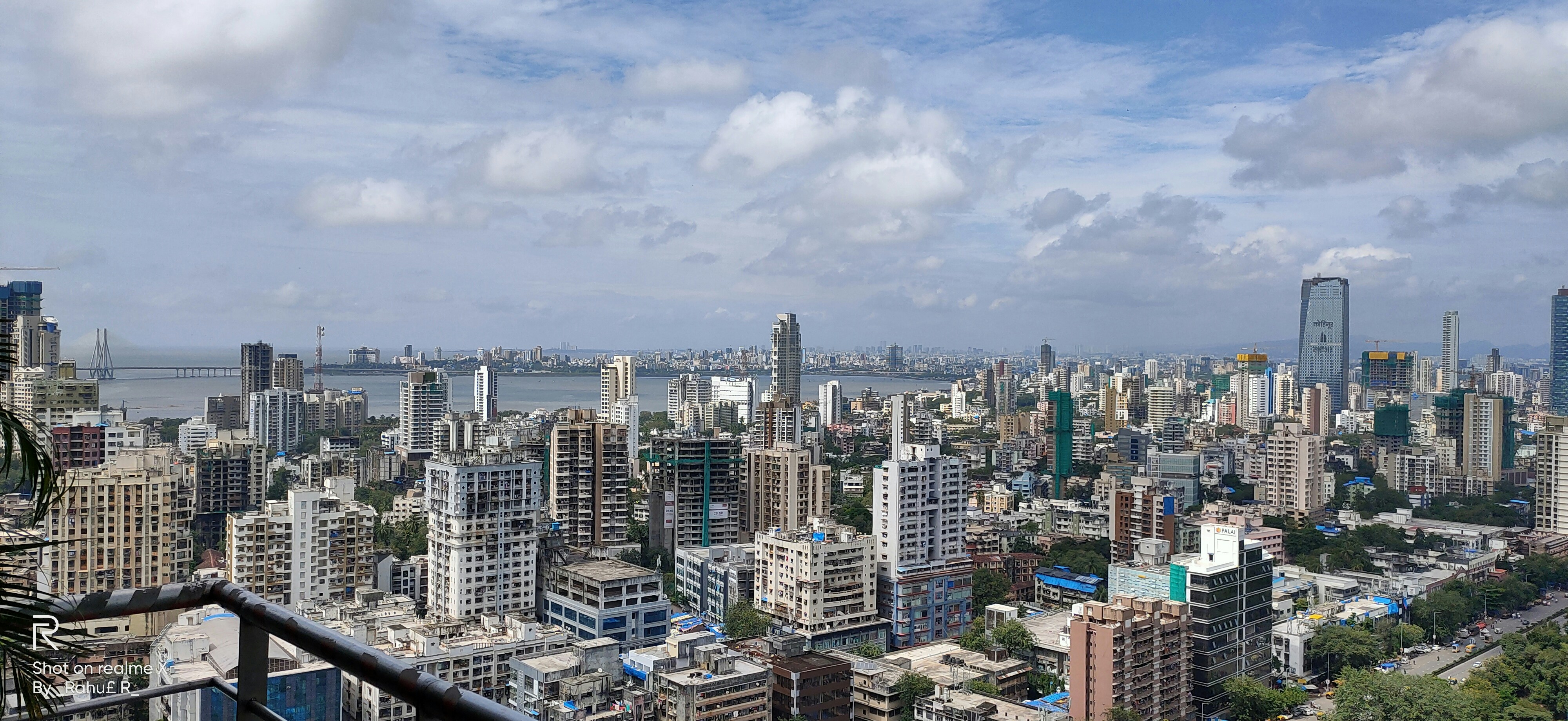 Vast cityscape showcasing Mumbai's diverse architecture and bustling urban life, with the coastline visible in the background.