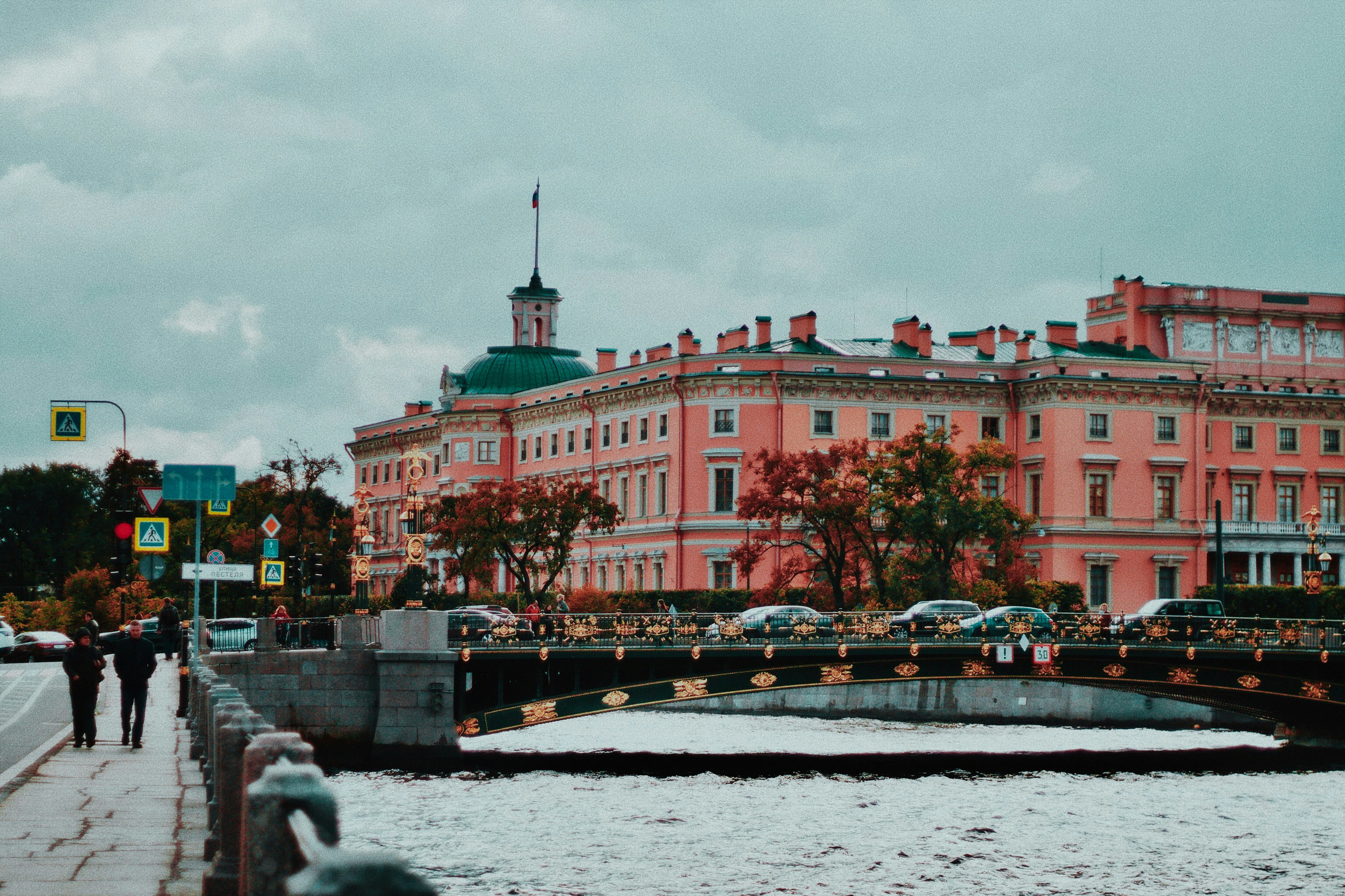Historic building adorned with autumn foliage alongside a river, with a decorative bridge in the foreground.