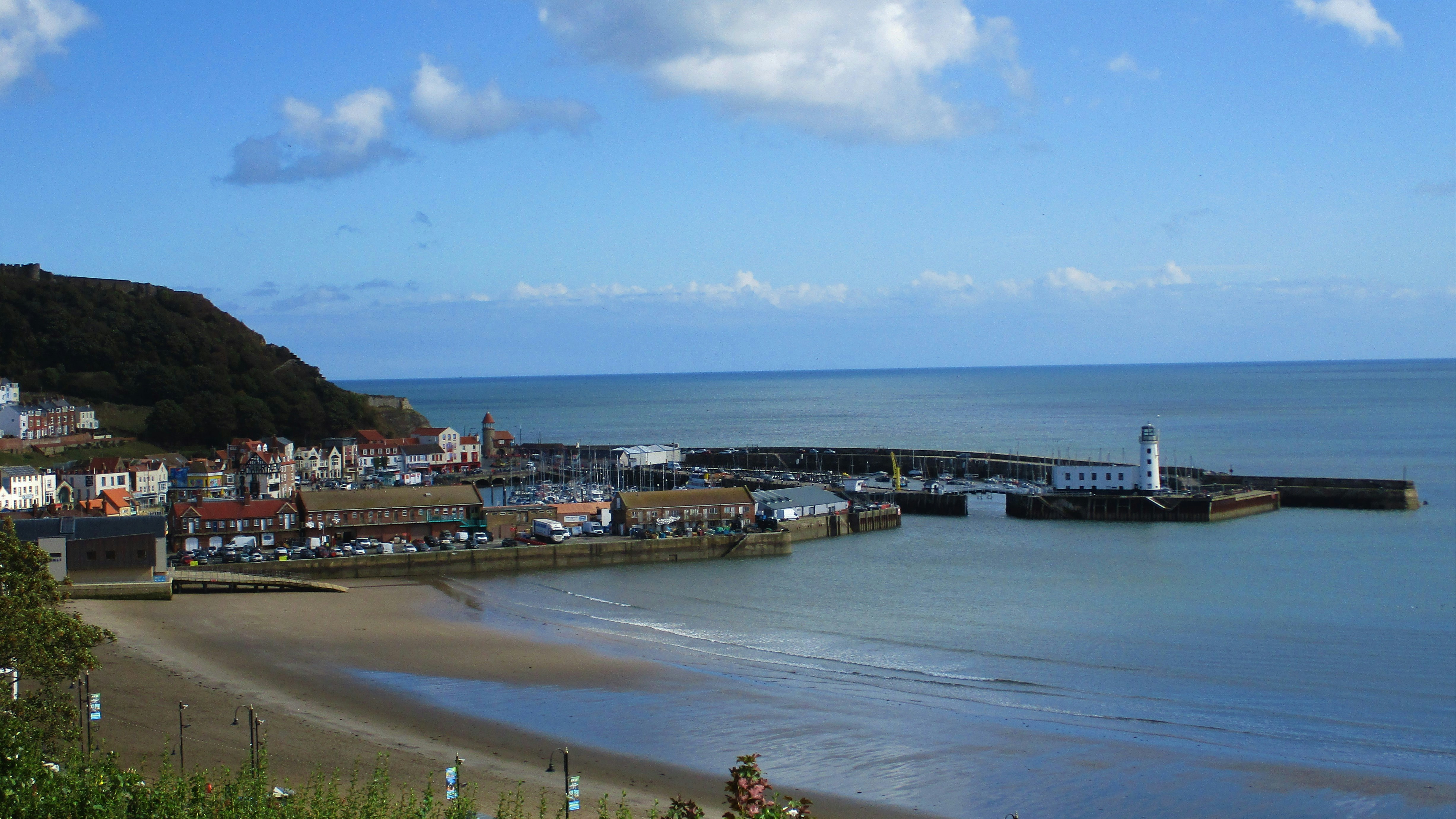 Scarborough's harbor with a rocky headland and lighthouse under a clear blue sky.