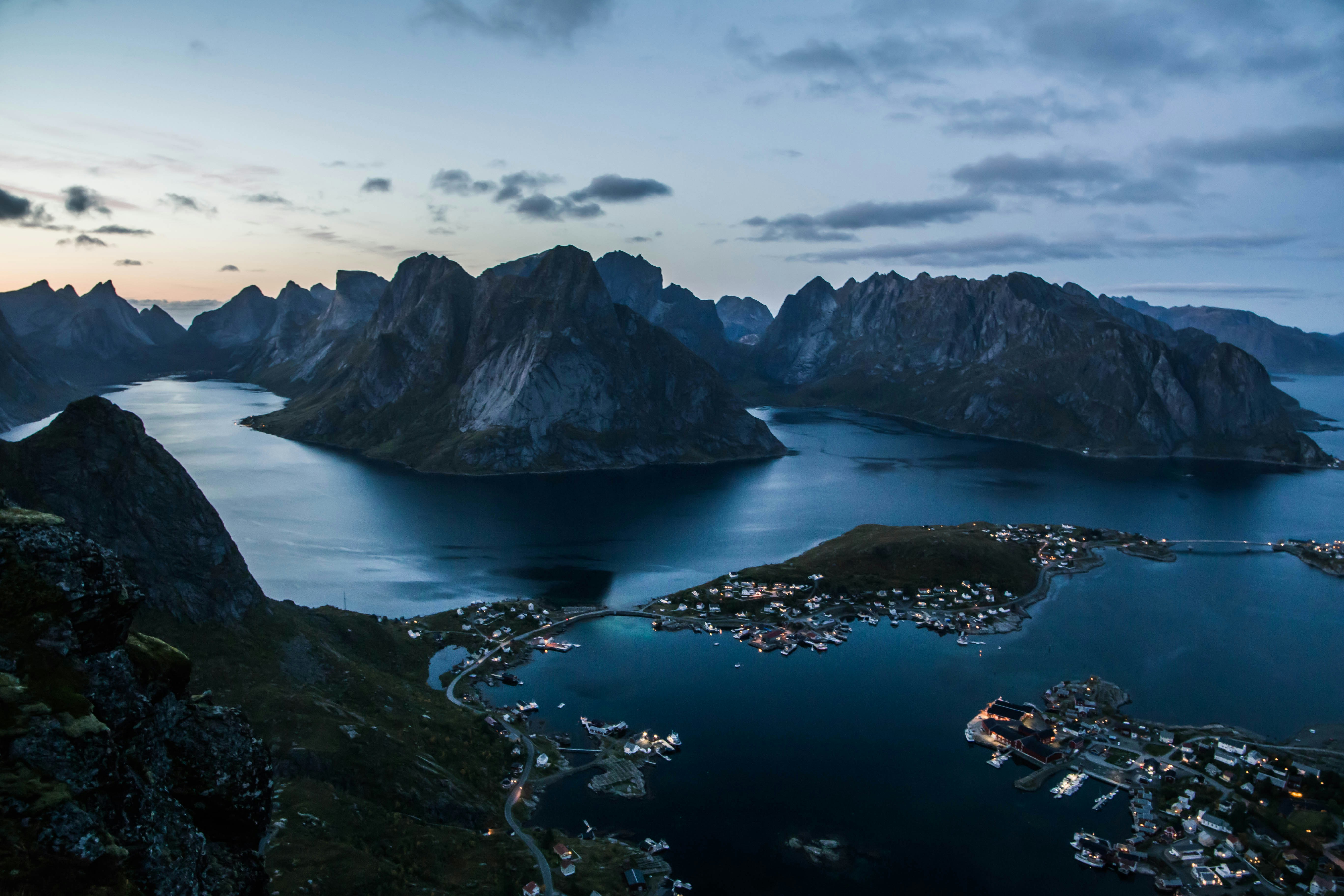 Mountainous landscape with a coastal town nestled between fjords at dusk.