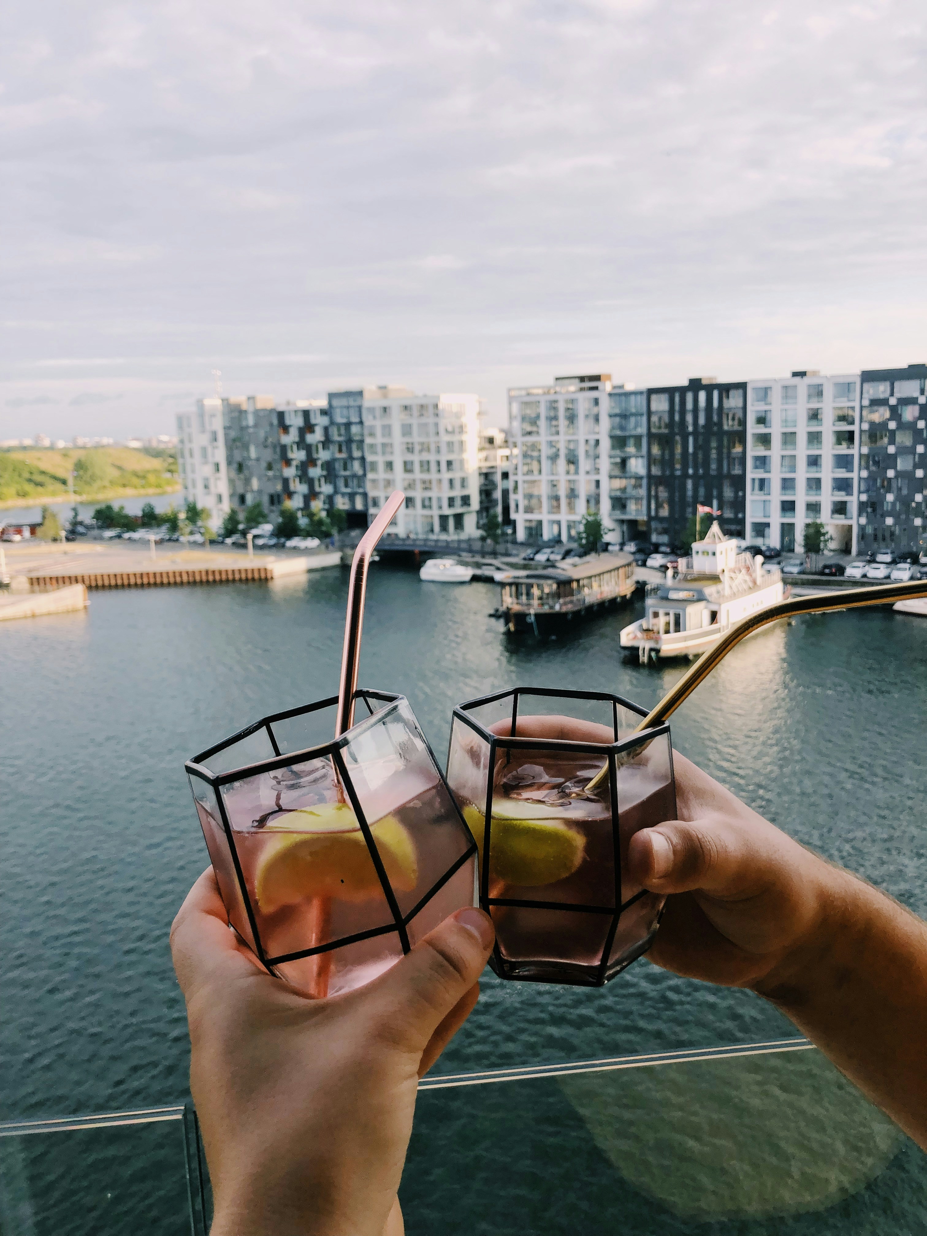 Two geometric glasses clink over a sunlit harbor