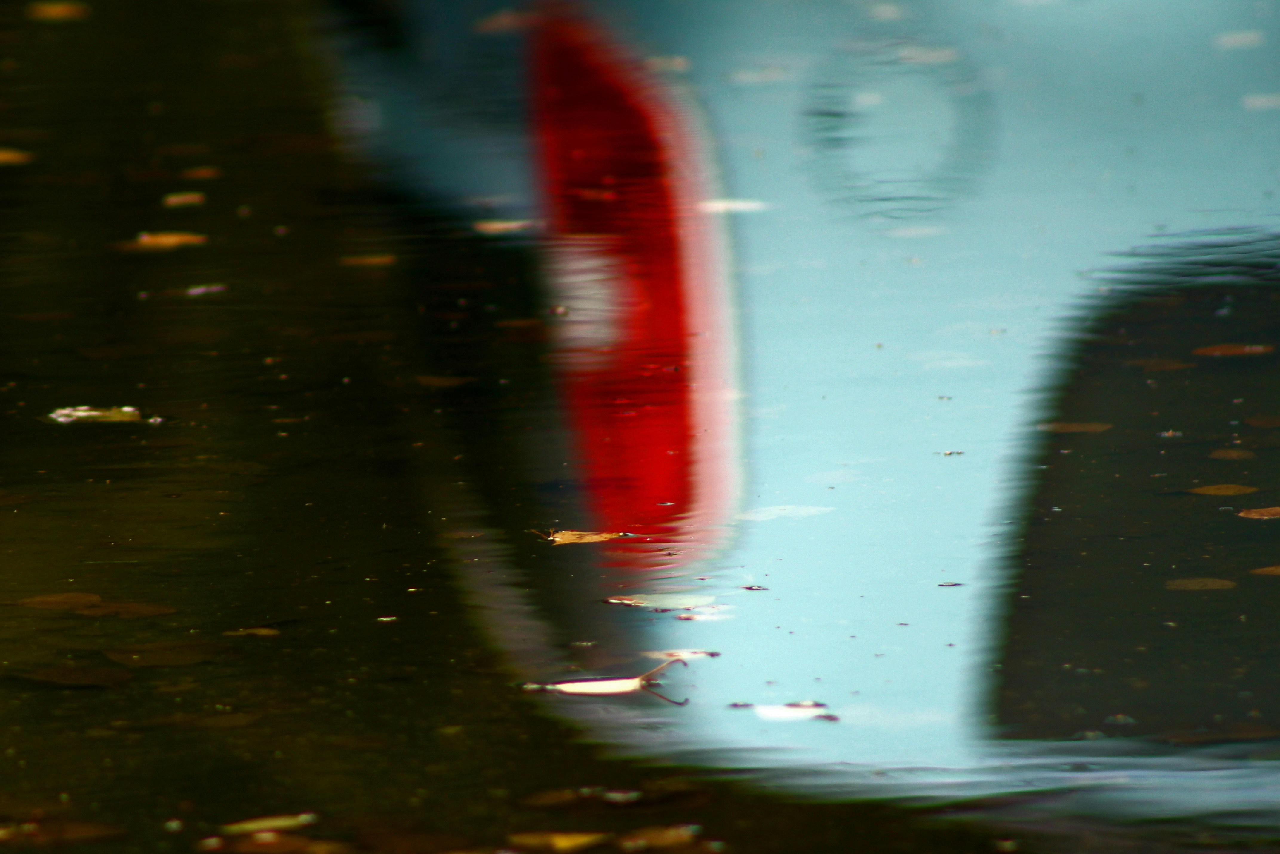 Abstract reflection of a red object in still water, creating a serene interplay of colors and shapes.