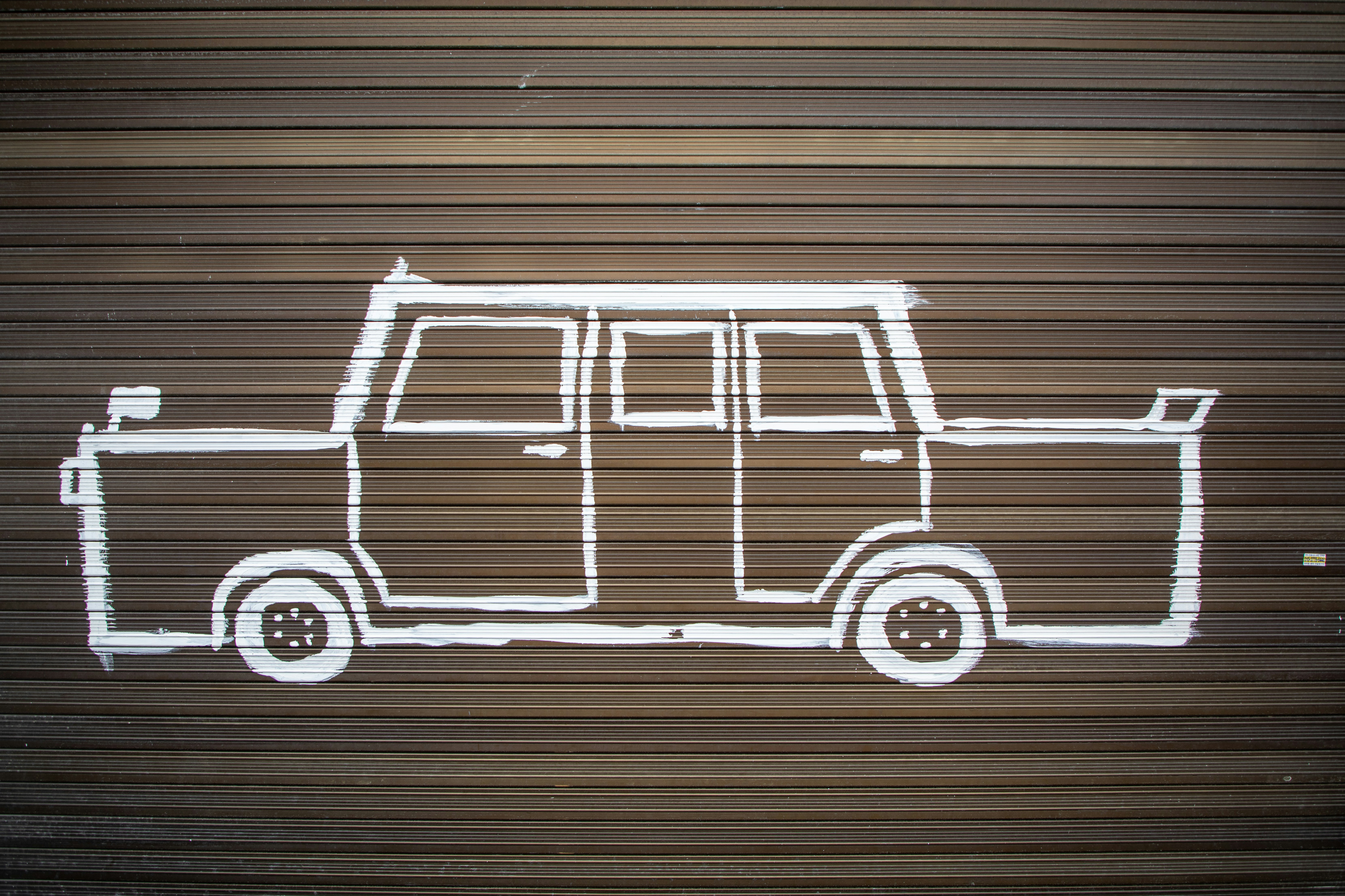 White outline of a pickup truck painted on a corrugated metal wall, showcasing urban street art. The minimalist design contrasts with the textured background.