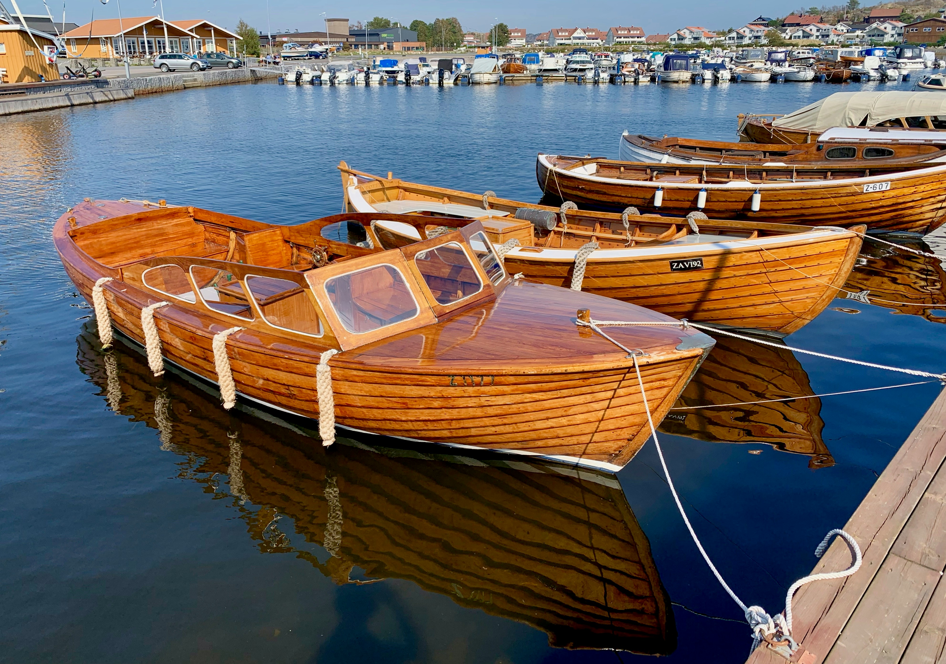 Polished wooden boats moored in a serene Norwegian harbor under clear skies.