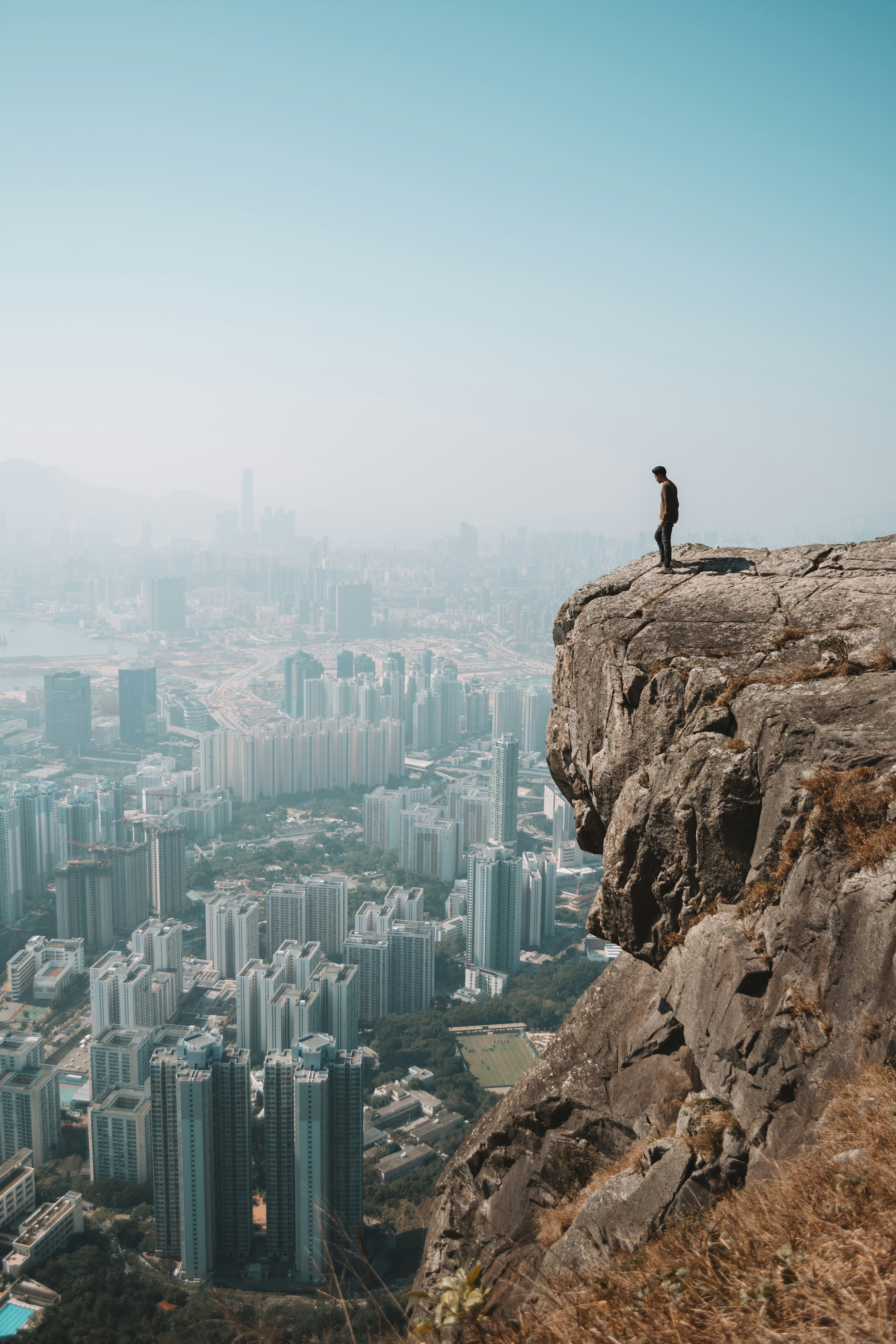 Edge of the City: Solitary figure atop a cliff above a sea of towers