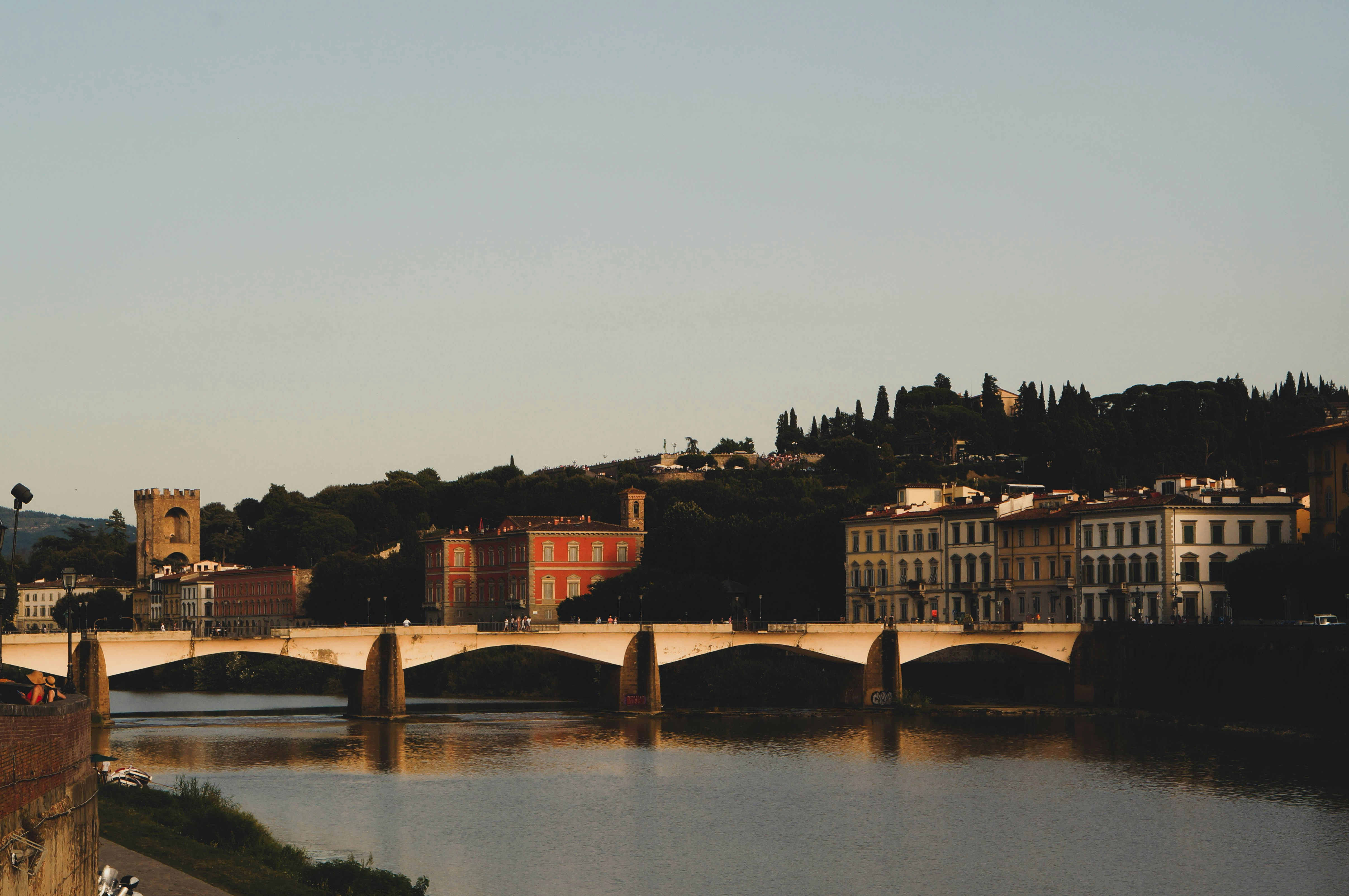 Historic bridge spanning the Arno River, framed by charming architecture and lush hills at dusk.