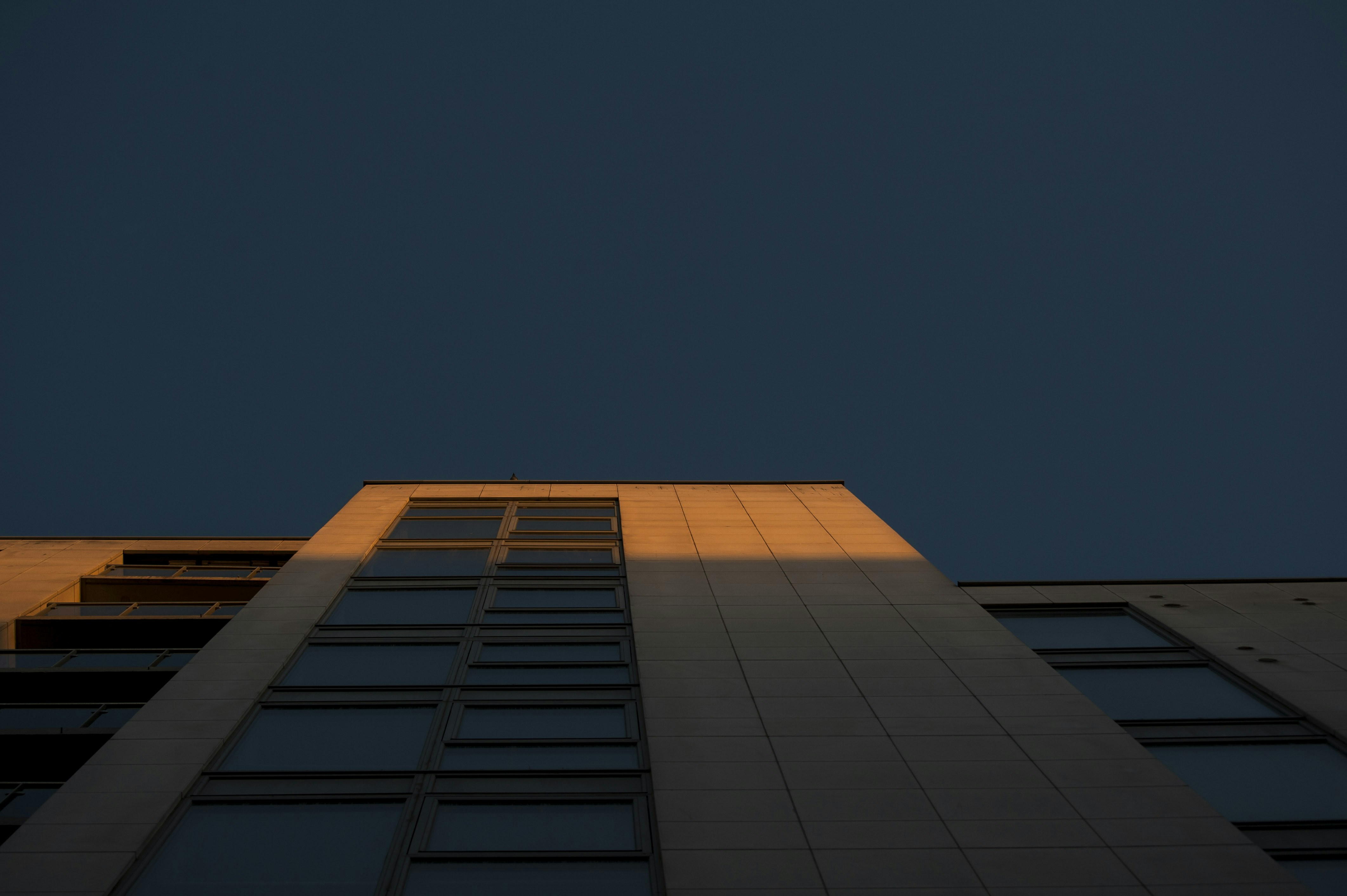 Modern building facade illuminated by the last rays of sunlight against a deepening twilight sky.