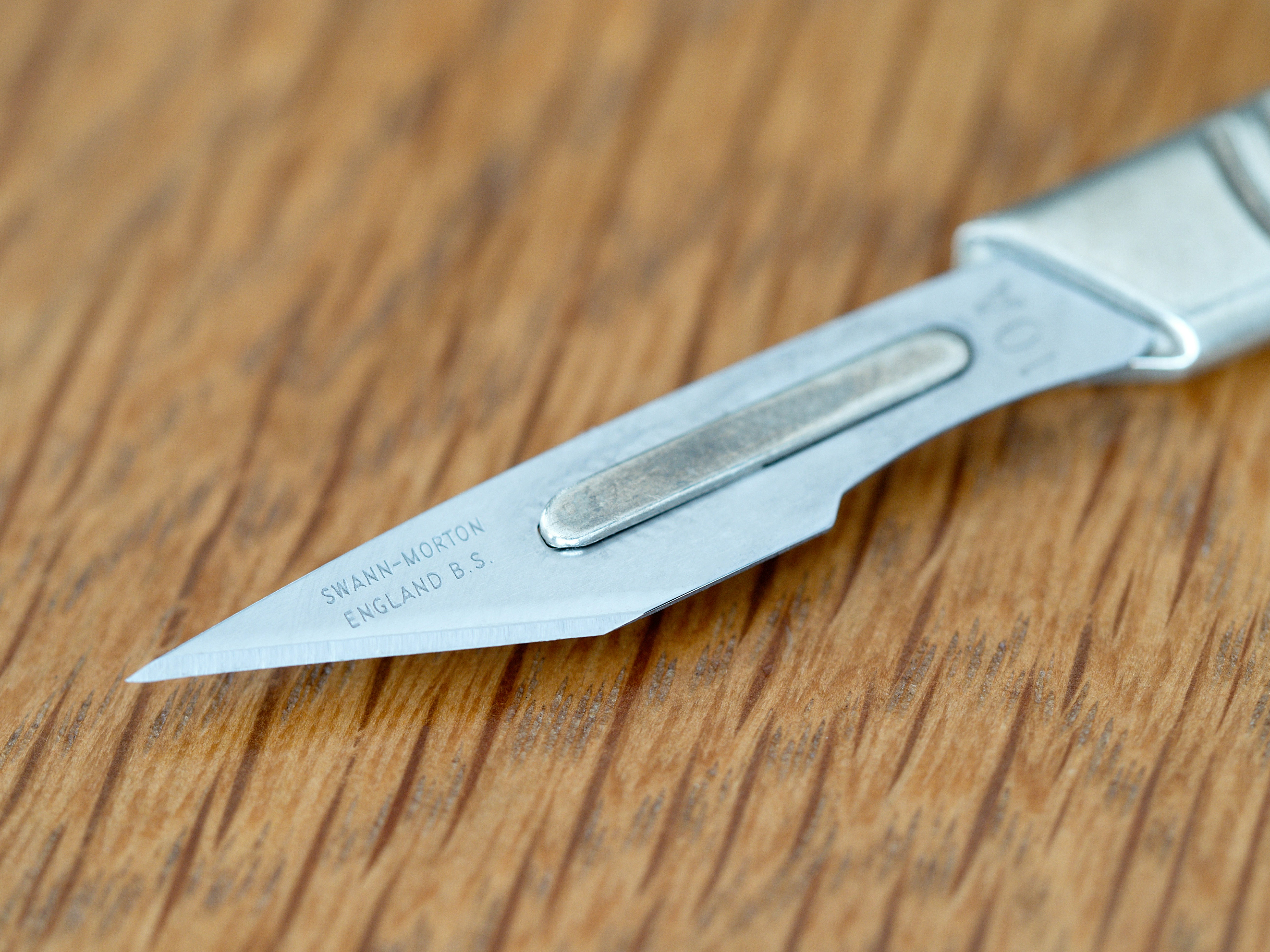 Close-up of a surgical scalpel blade resting on a wooden surface, showcasing intricate details and craftsmanship.