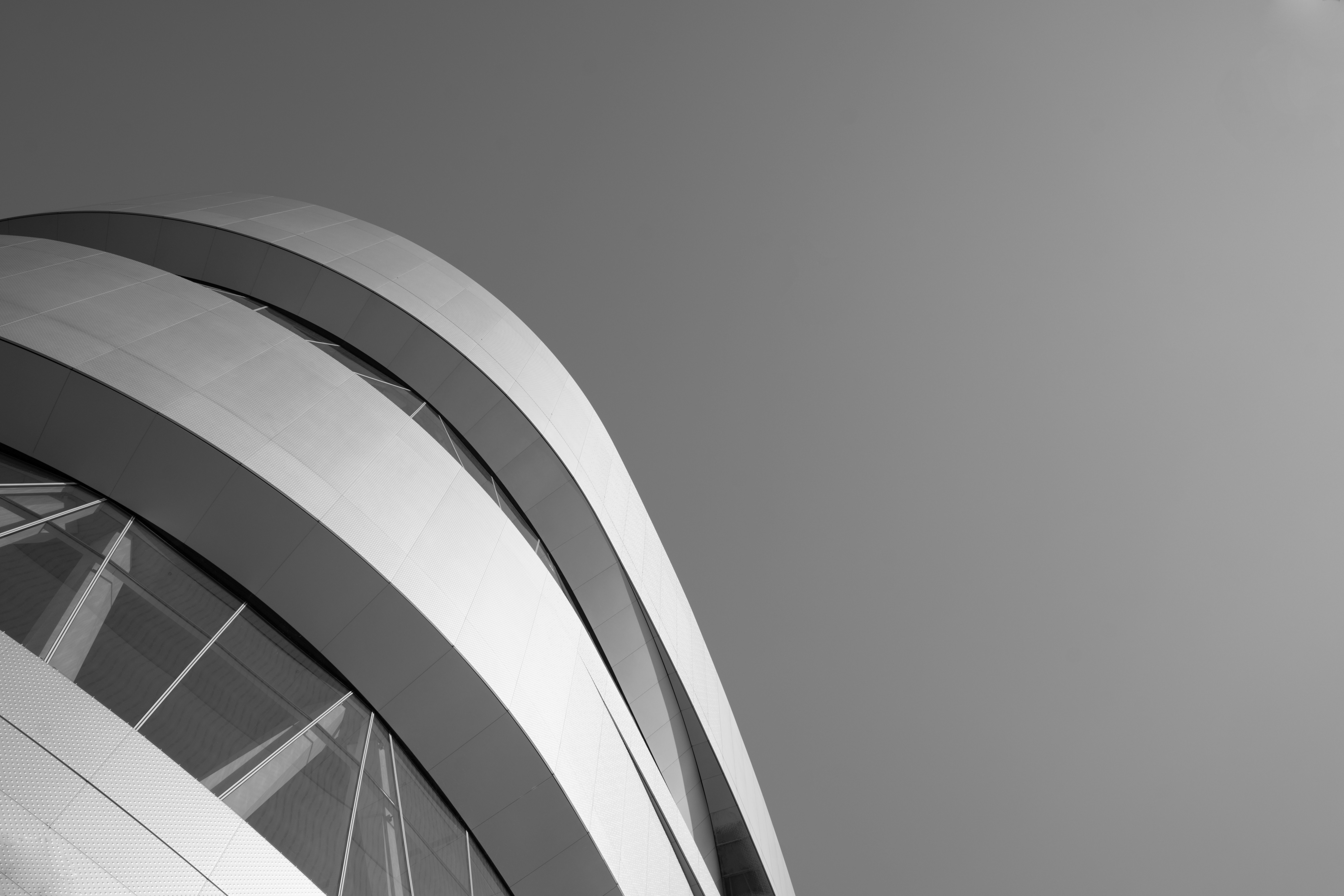 Dynamic architectural structure with sweeping curves and glass elements against a monochromatic sky.