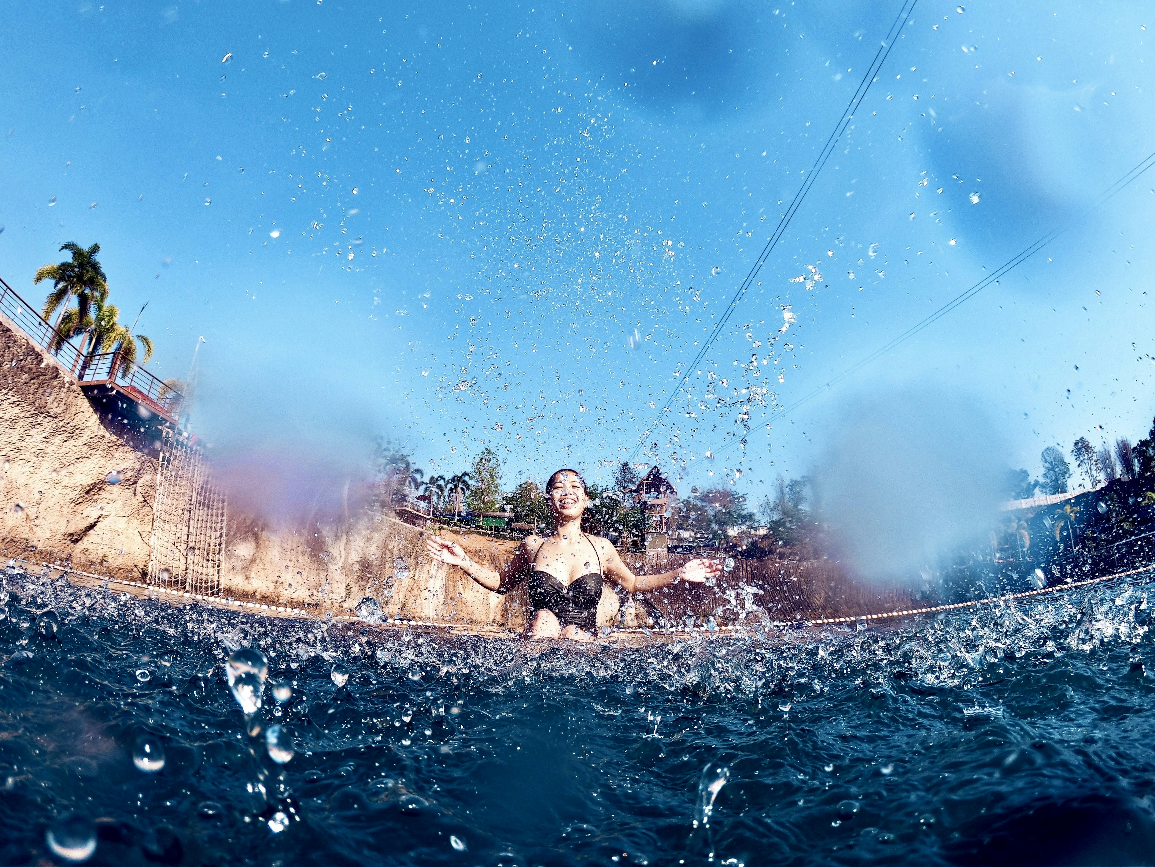 Child joyfully splashing in a pool, surrounded by water droplets and a vibrant blue sky. The scene captures the essence of summer playfulness.
