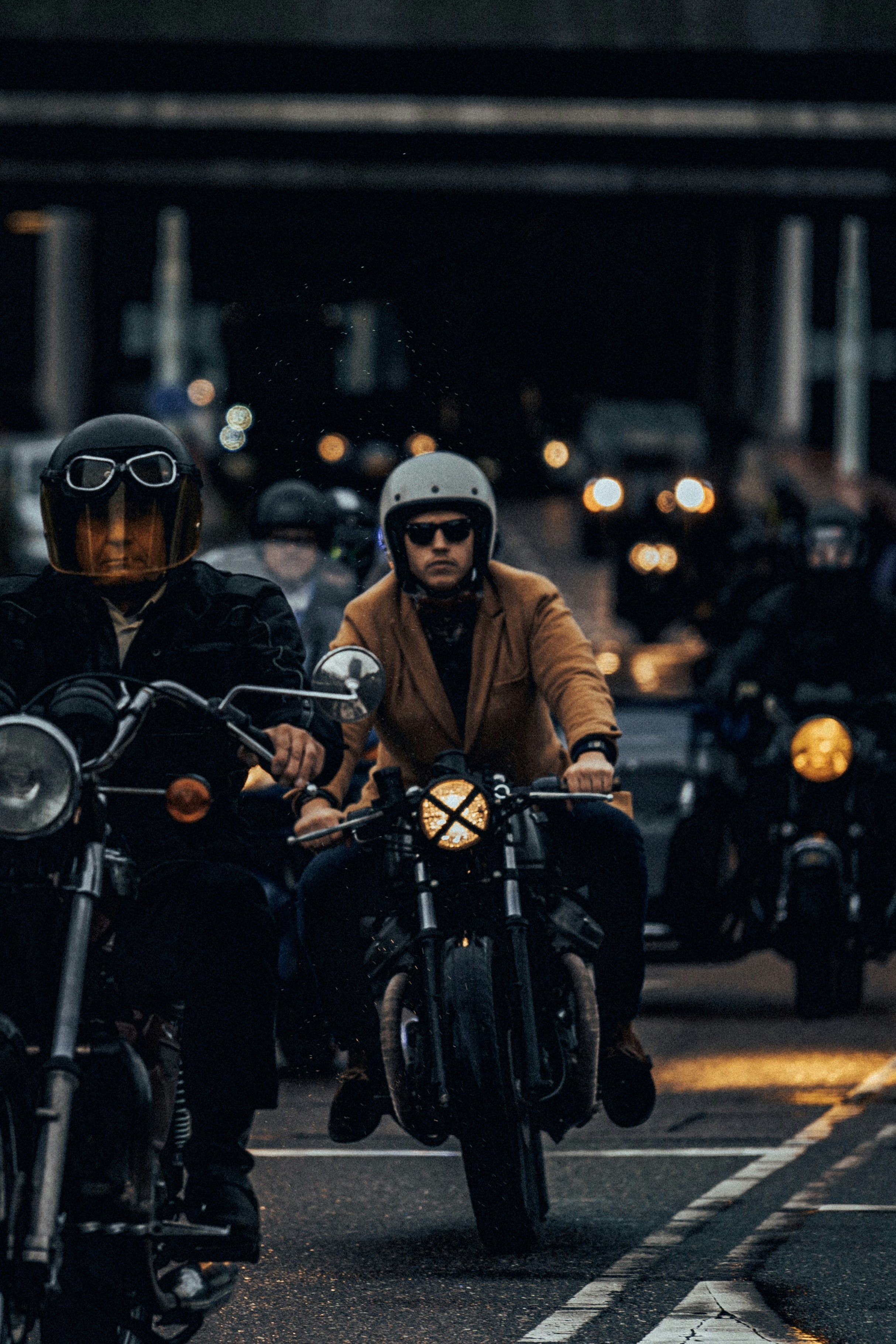 Motorcycle riders navigate a bustling city street, showcasing their unique styles and camaraderie under the evening lights.