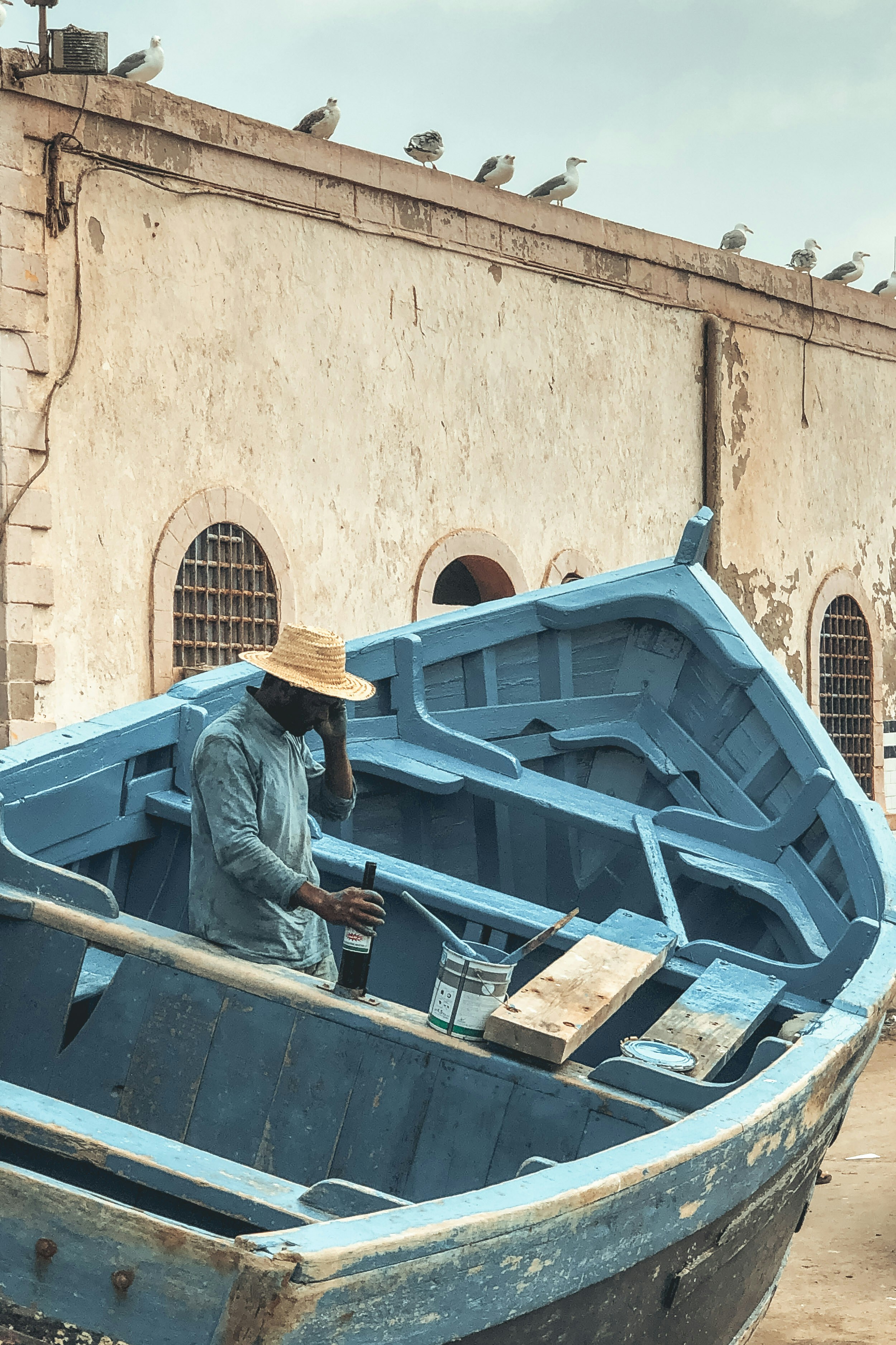 Blue Dory by a Weathered Wharf Wall, a Straw-Hatted Worker at the Helm