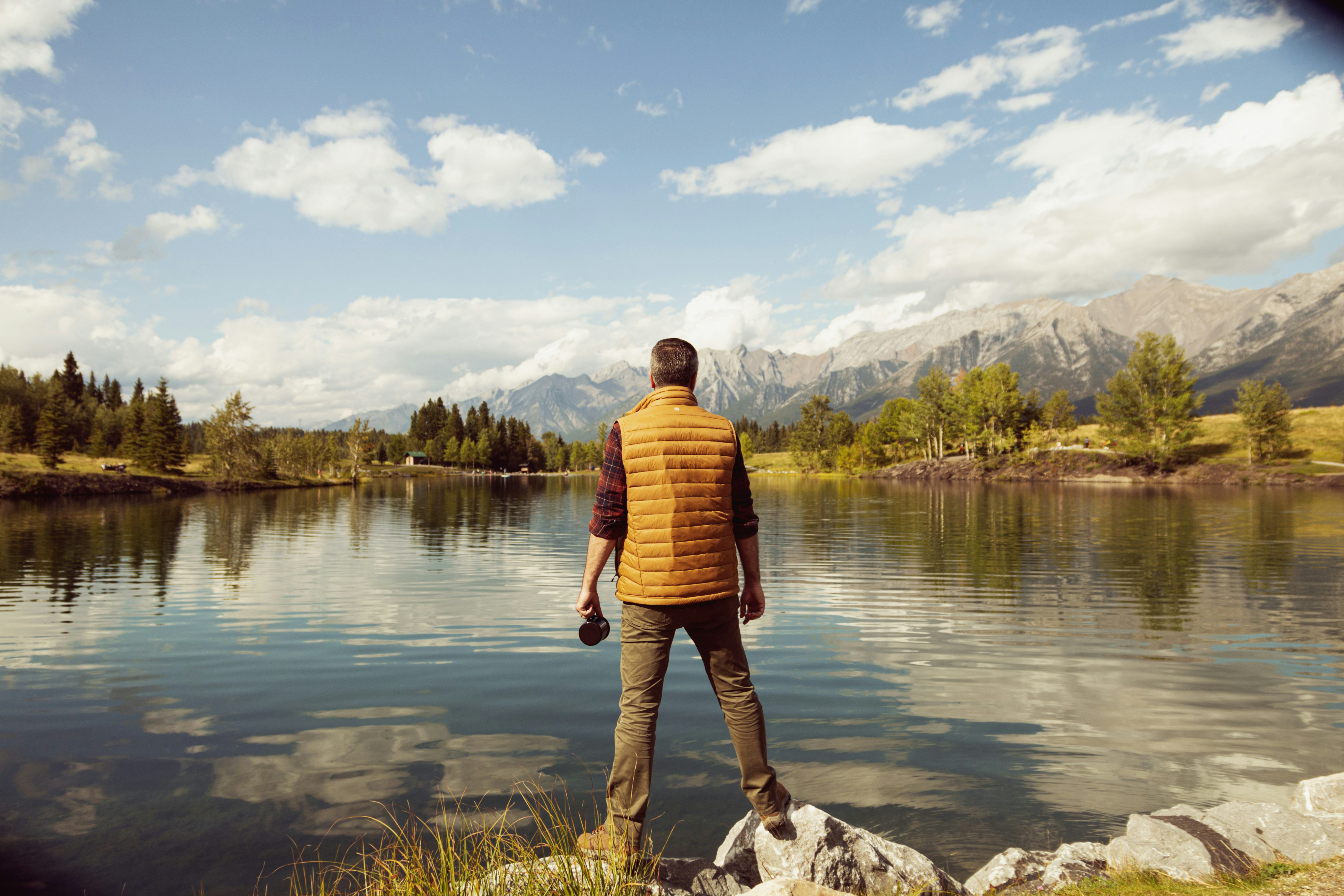 Orange-vested Wanderer Framed by Alpine Lake and Snow-Capped Peaks