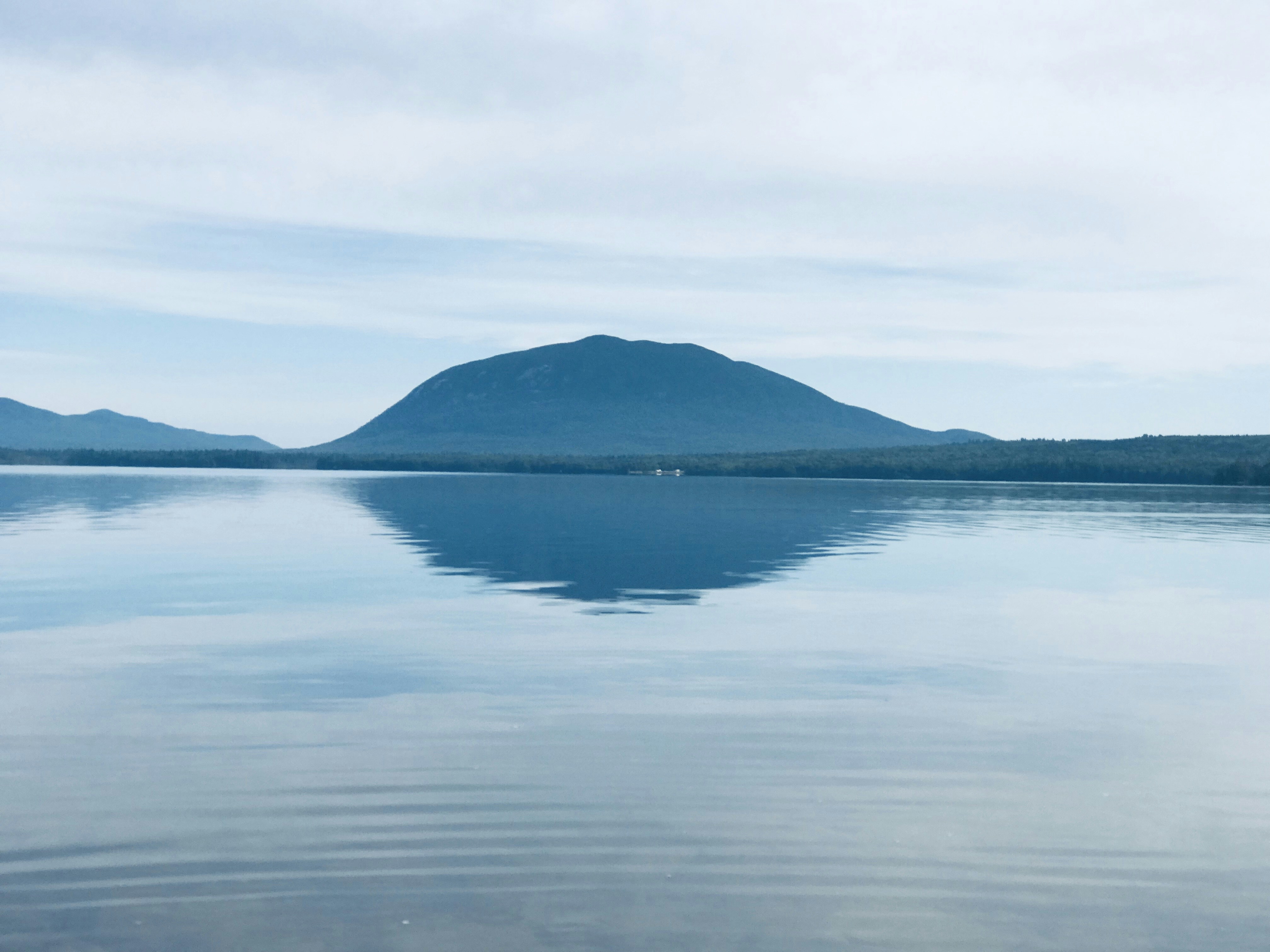 Calm lake waters mirror distant mountains under a soft, cloudy sky.