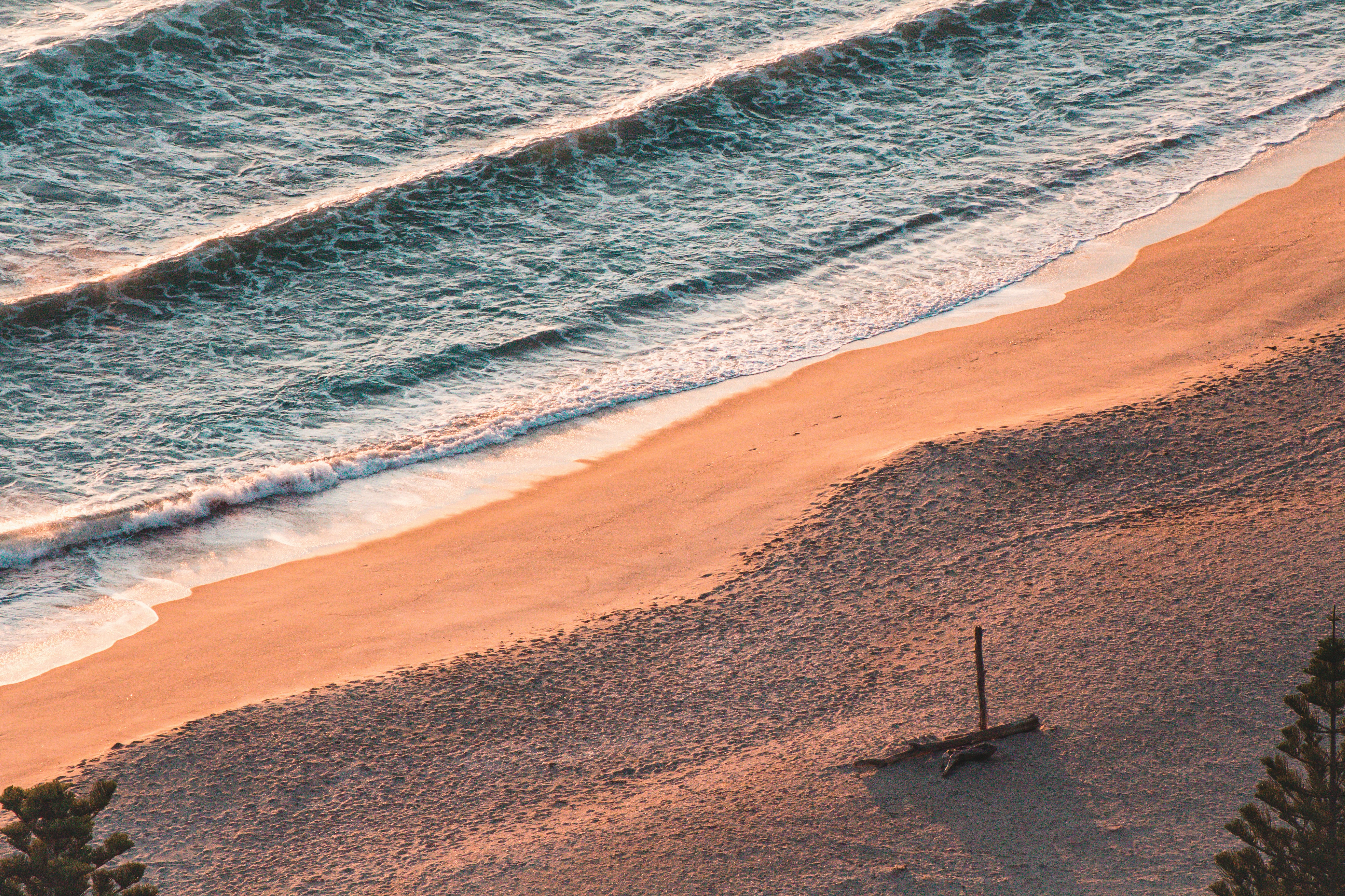 Gentle waves lap against a sunlit sandy beach, casting a warm glow at dusk.