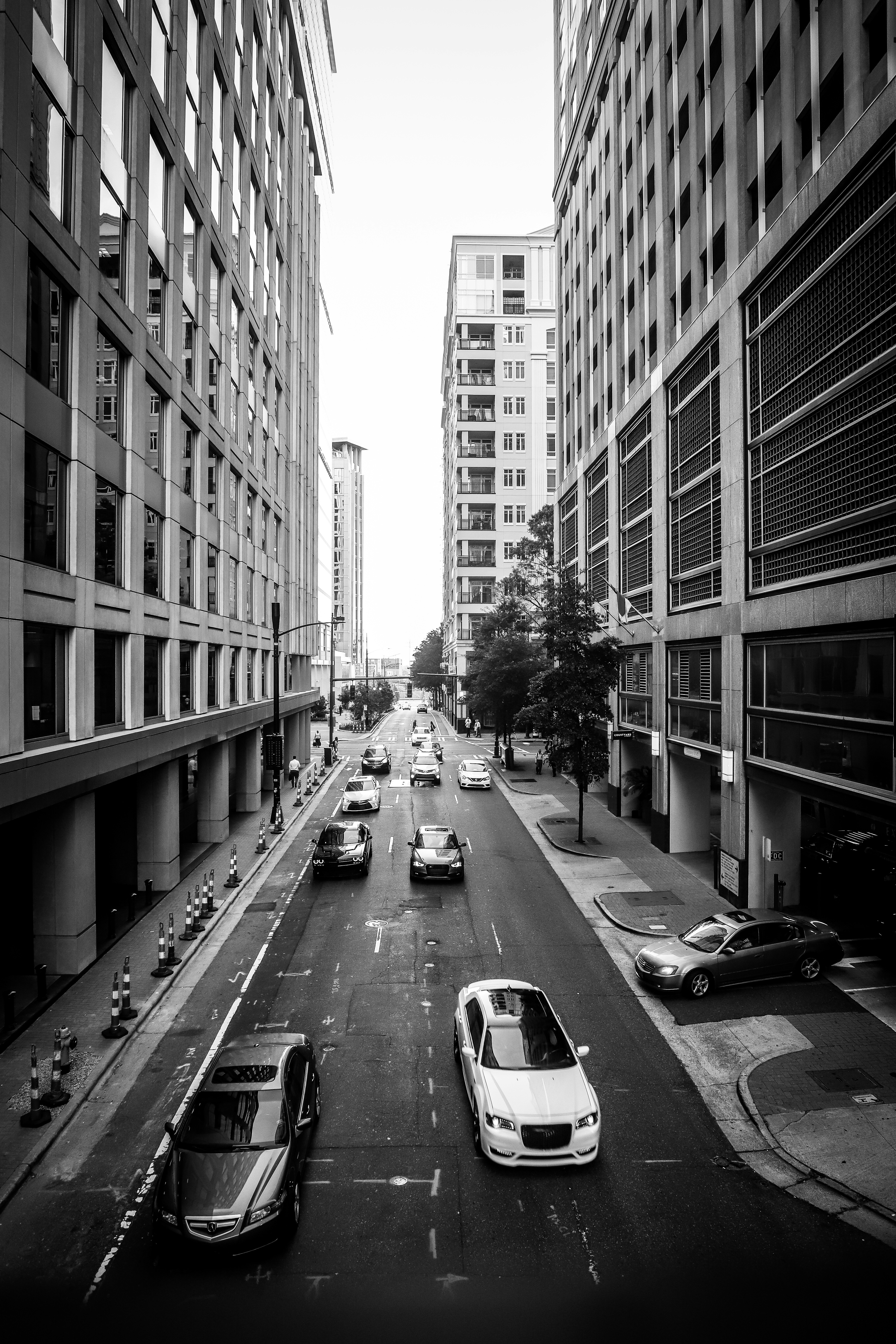 A bustling city street captured in black and white, showcasing vehicles navigating through towering buildings. The scene conveys the rhythm of urban life.