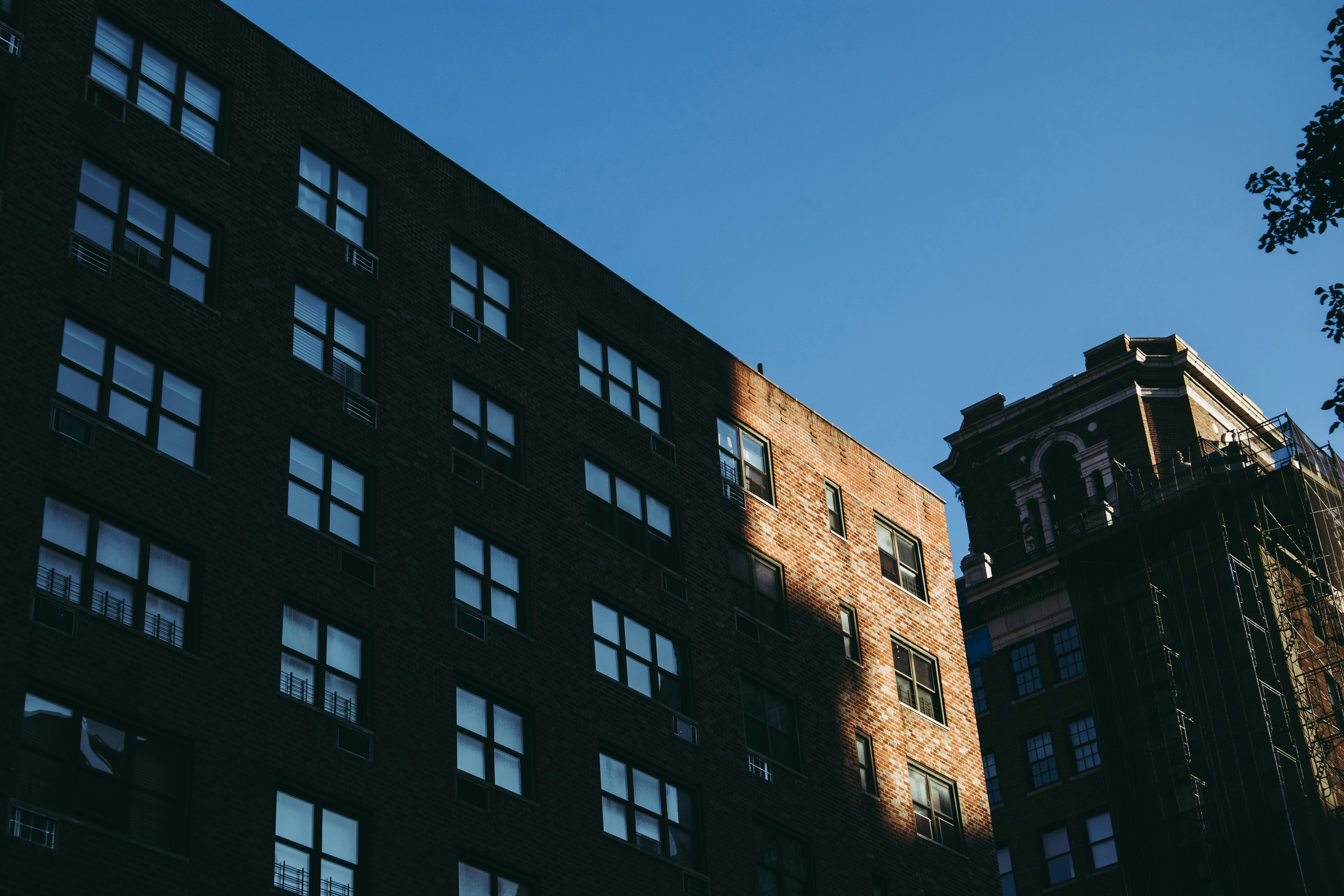 Sunlight casts dramatic shadows on a cluster of brick buildings, highlighting their architectural features against a clear blue sky.