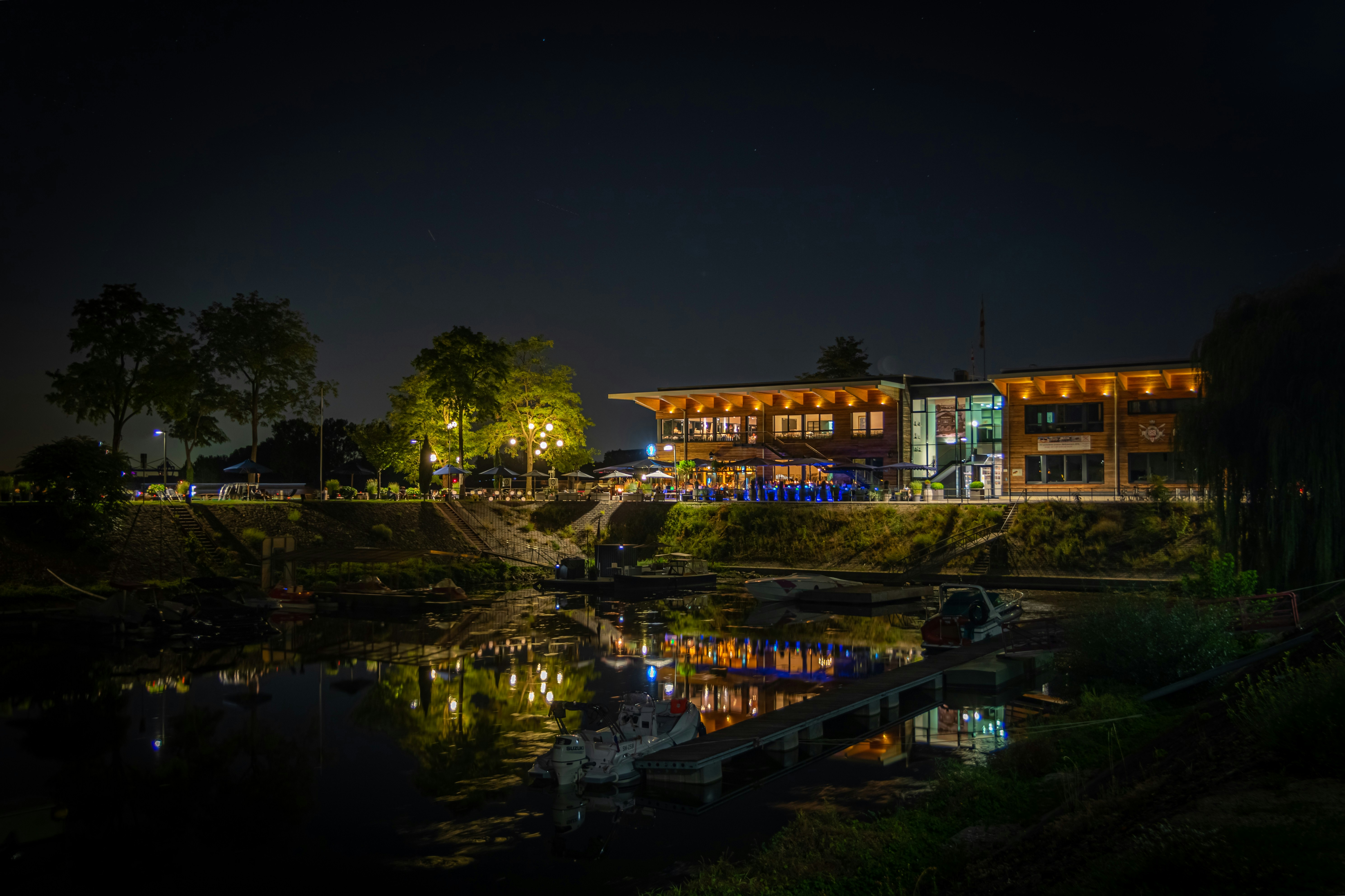Modern building illuminated by warm lights reflecting on a calm lake at night.