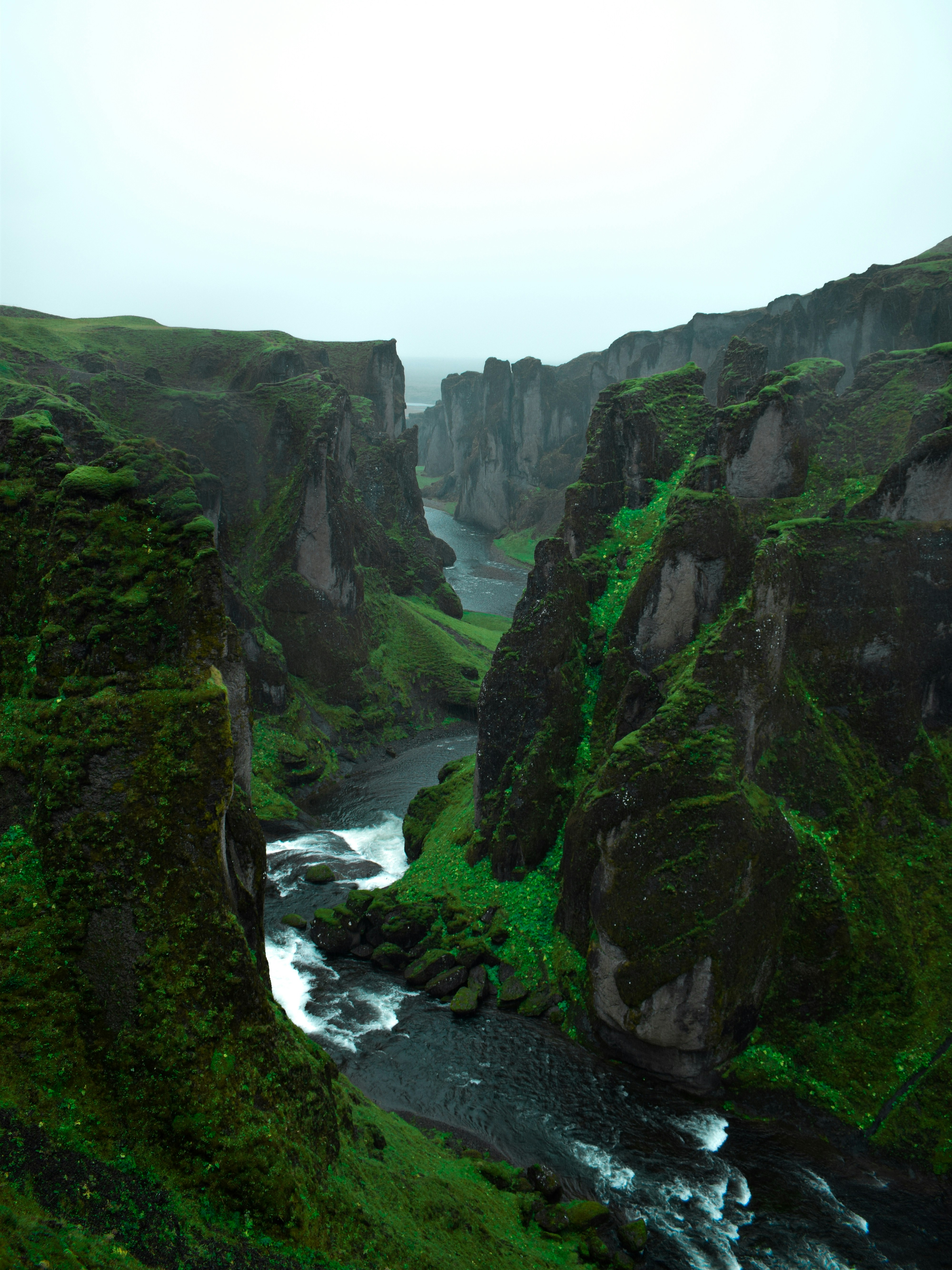Vast green cliffs frame a winding river, showcasing the dramatic geology of the landscape. Mist shrouds the scene, adding an air of mystery.