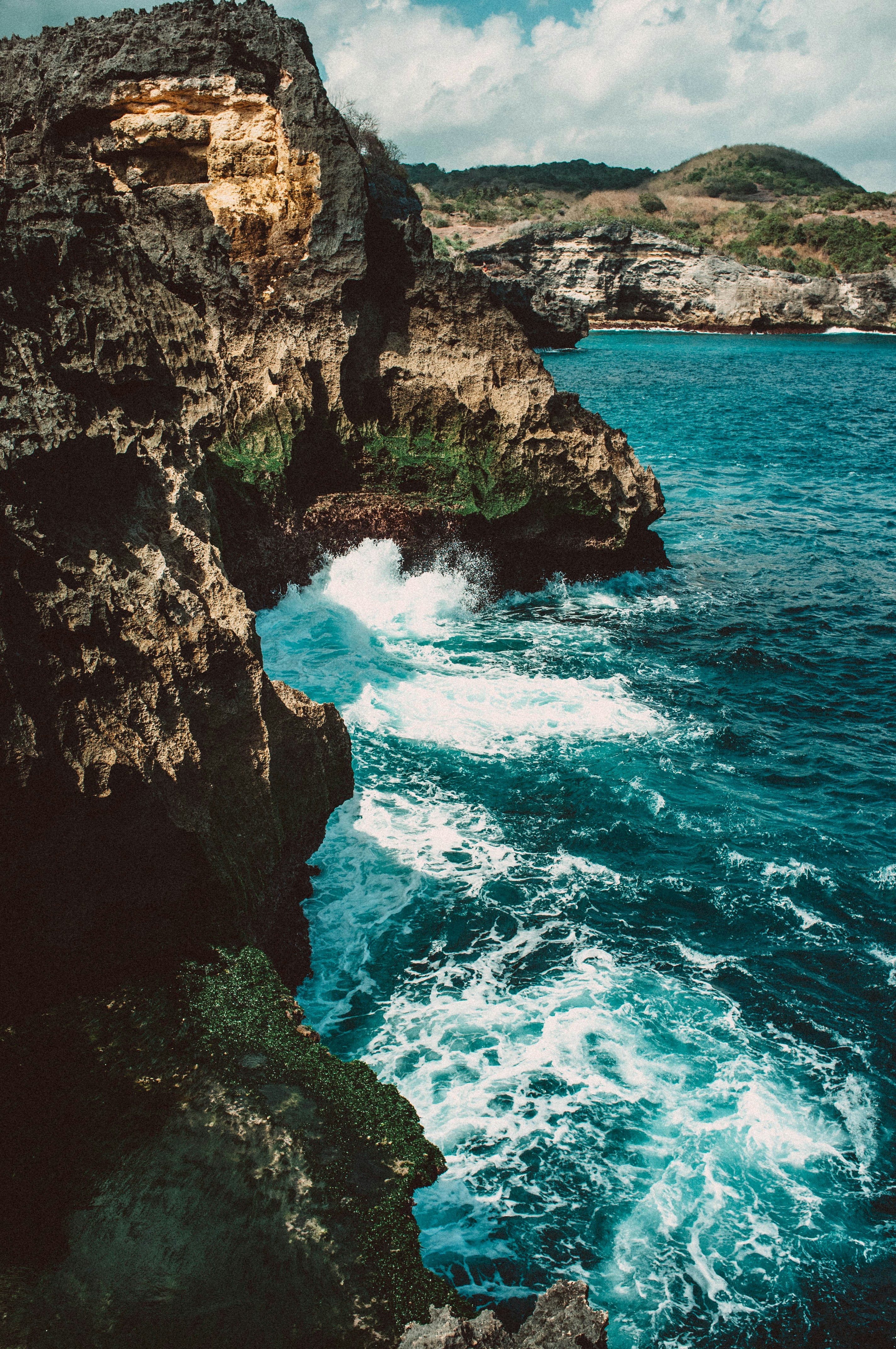 Waves crashing against rugged cliffs under a partly cloudy sky.