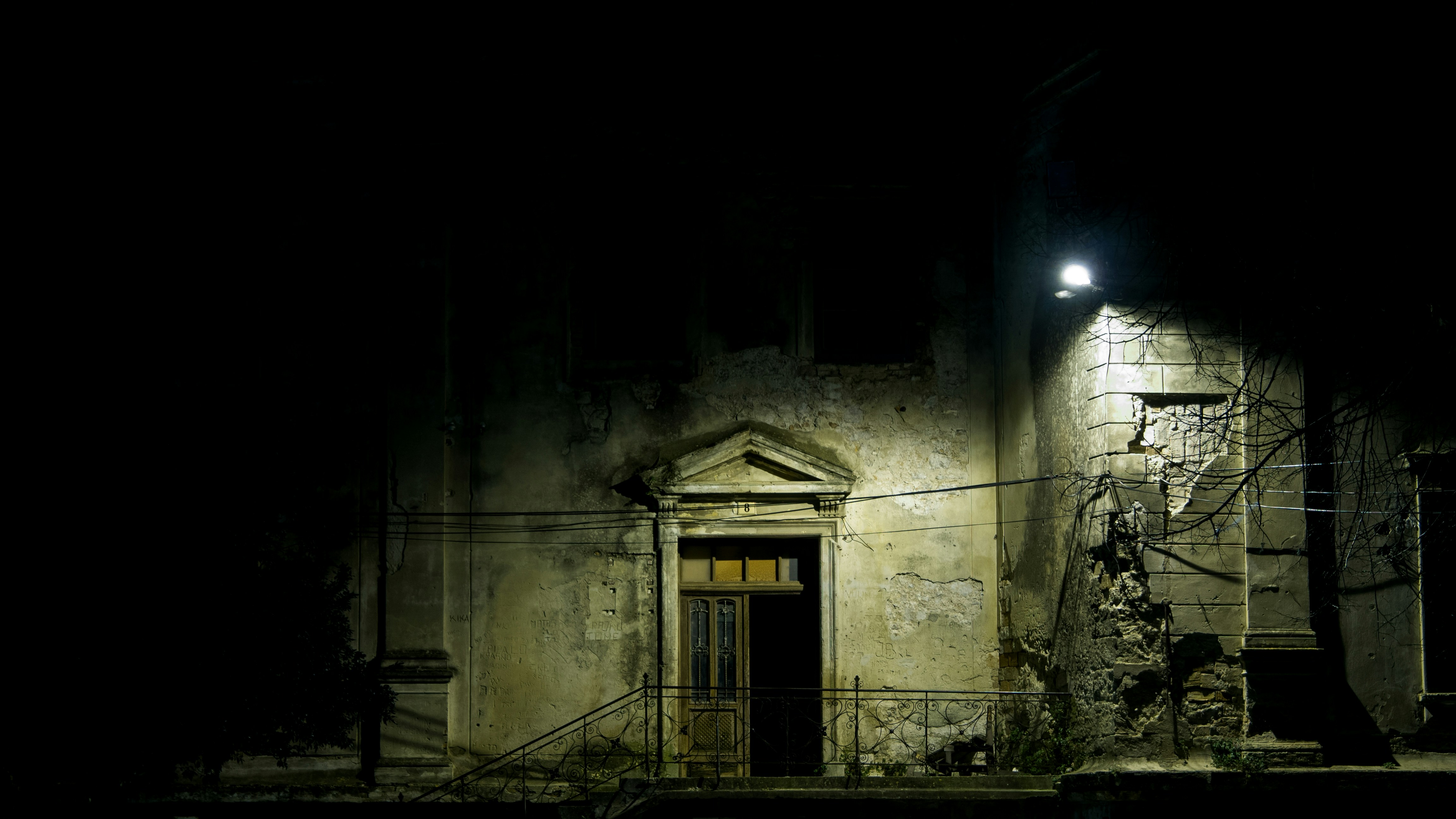 Weathered entrance of an abandoned building illuminated by a solitary streetlight, showcasing peeling paint and crumbling walls.
