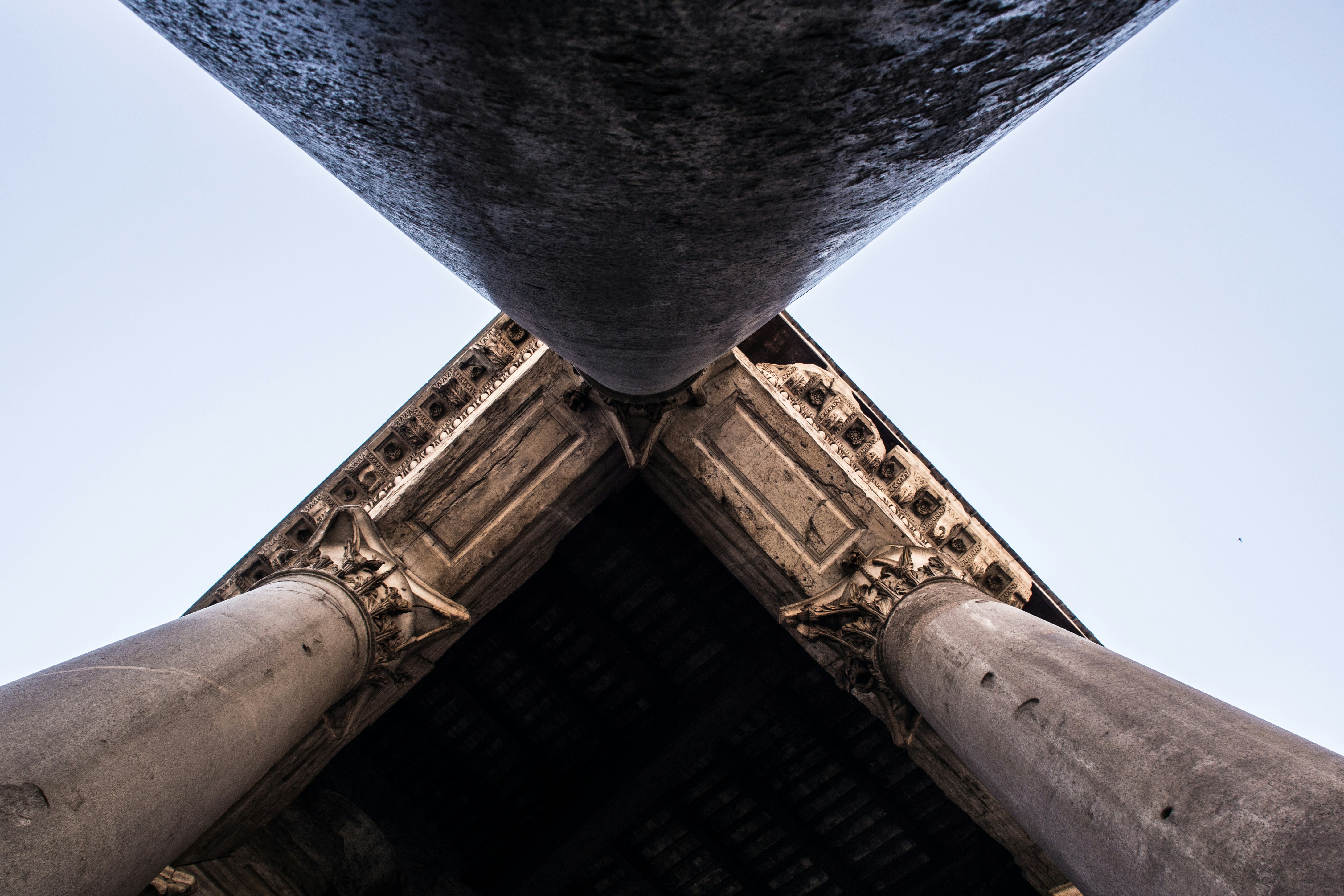 View from beneath ancient columns, showcasing intricate details and the sky above. The perspective highlights the grandeur of classical architecture.