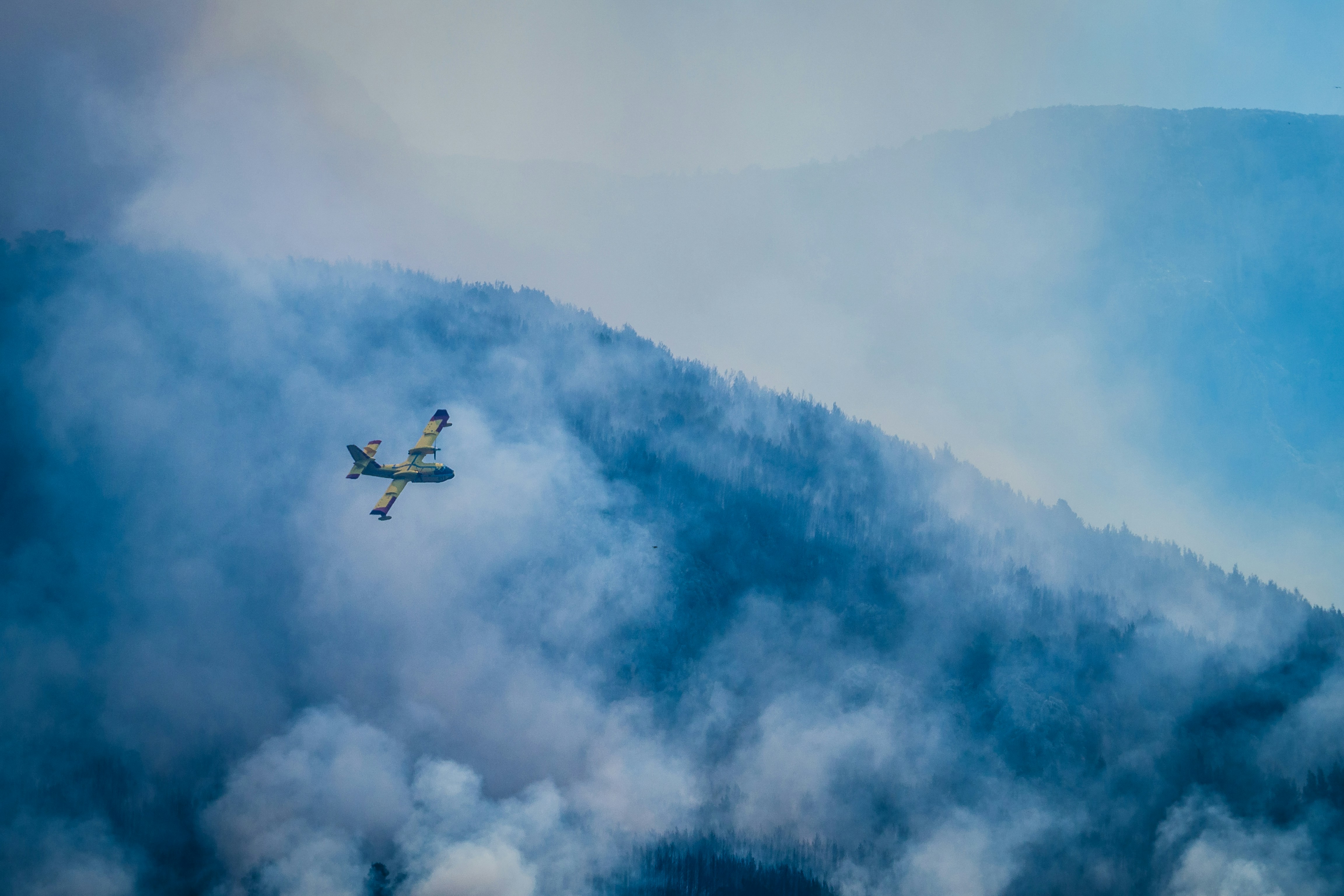 Yellow Water Bomber Through Veiled Blue Smoke Over a Mountain Ridge