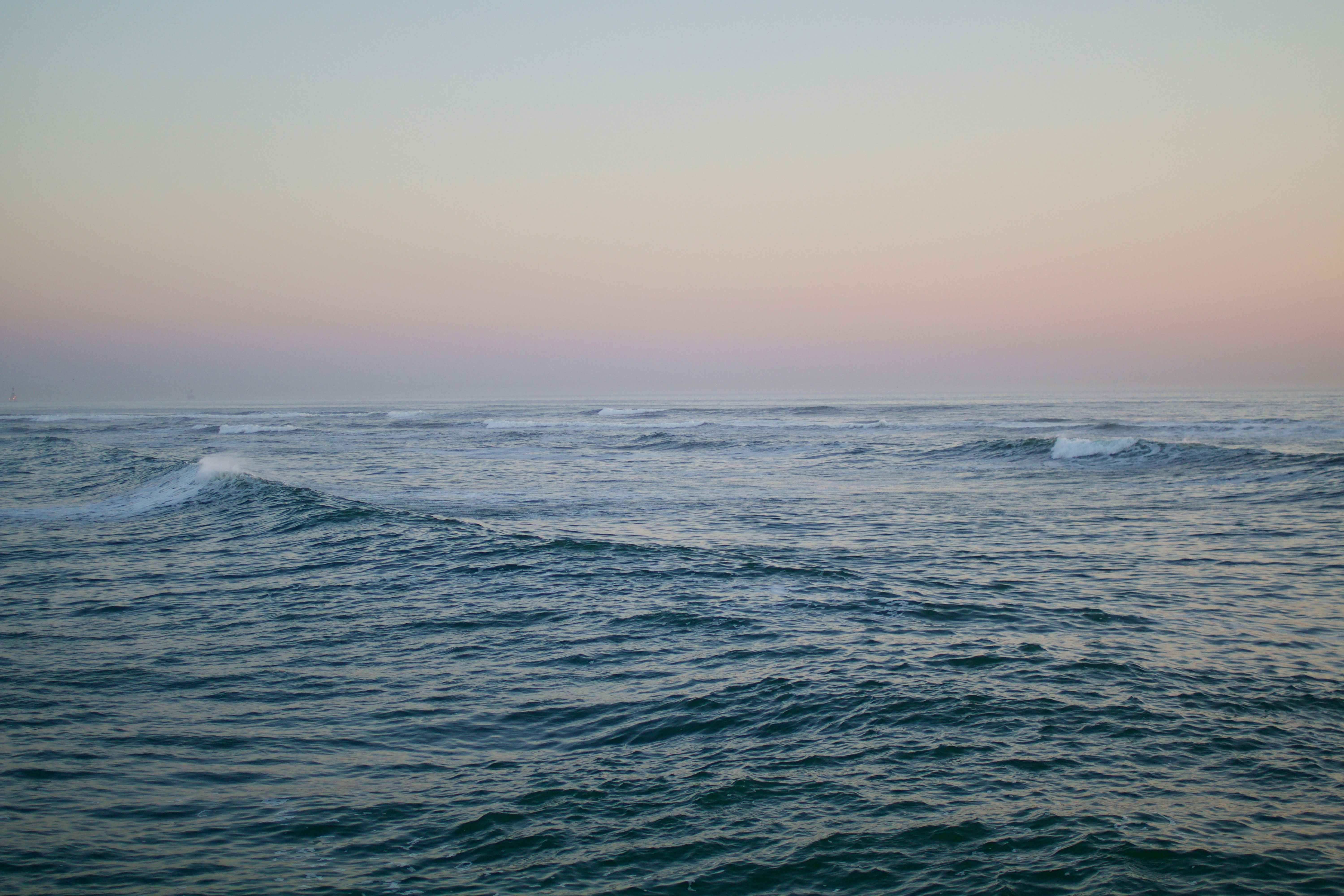 Gentle waves ripple across a tranquil ocean under a pastel sky at dusk.