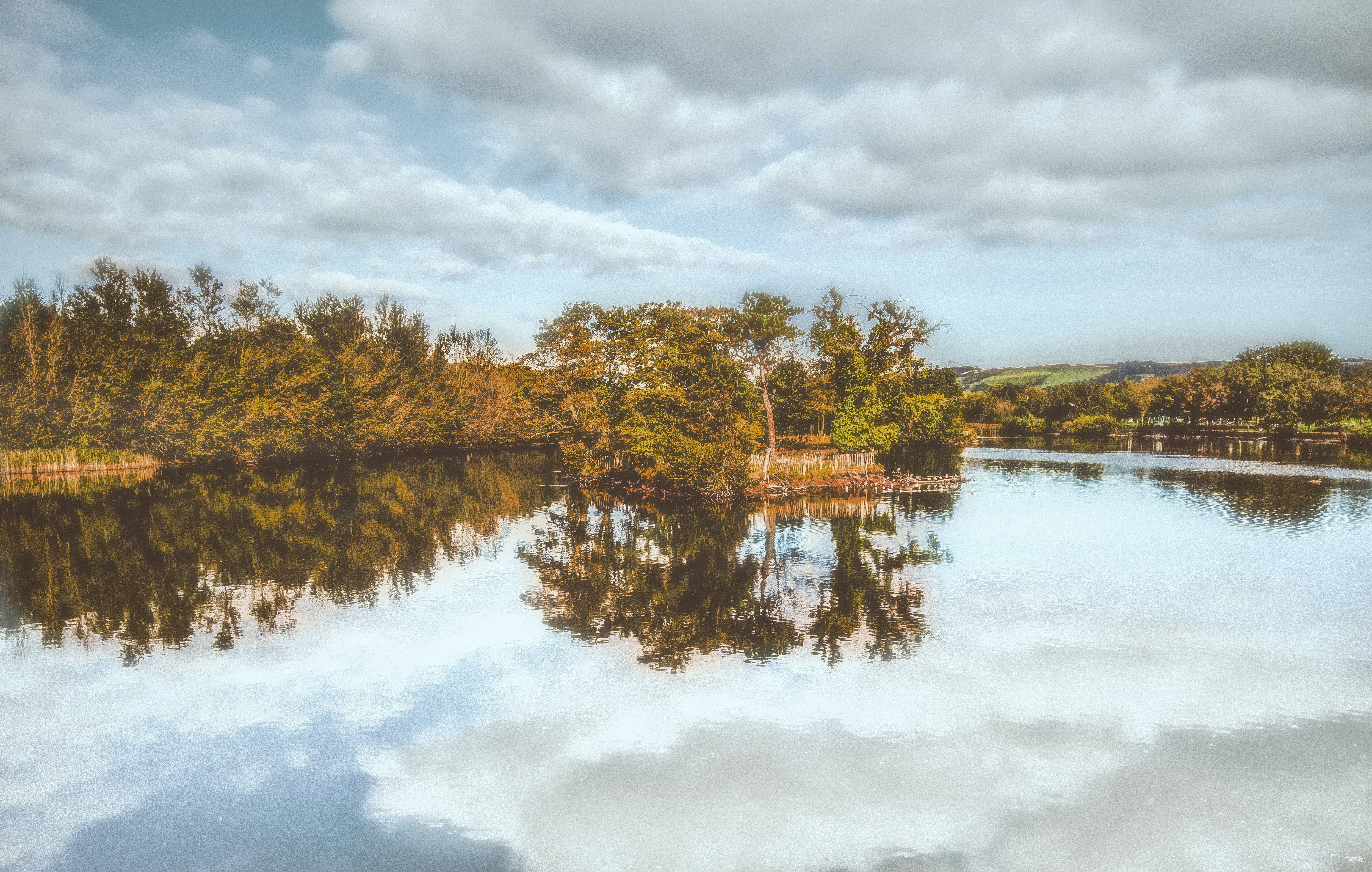 Serene river reflecting lush trees and a cloudy sky on an autumn day.
