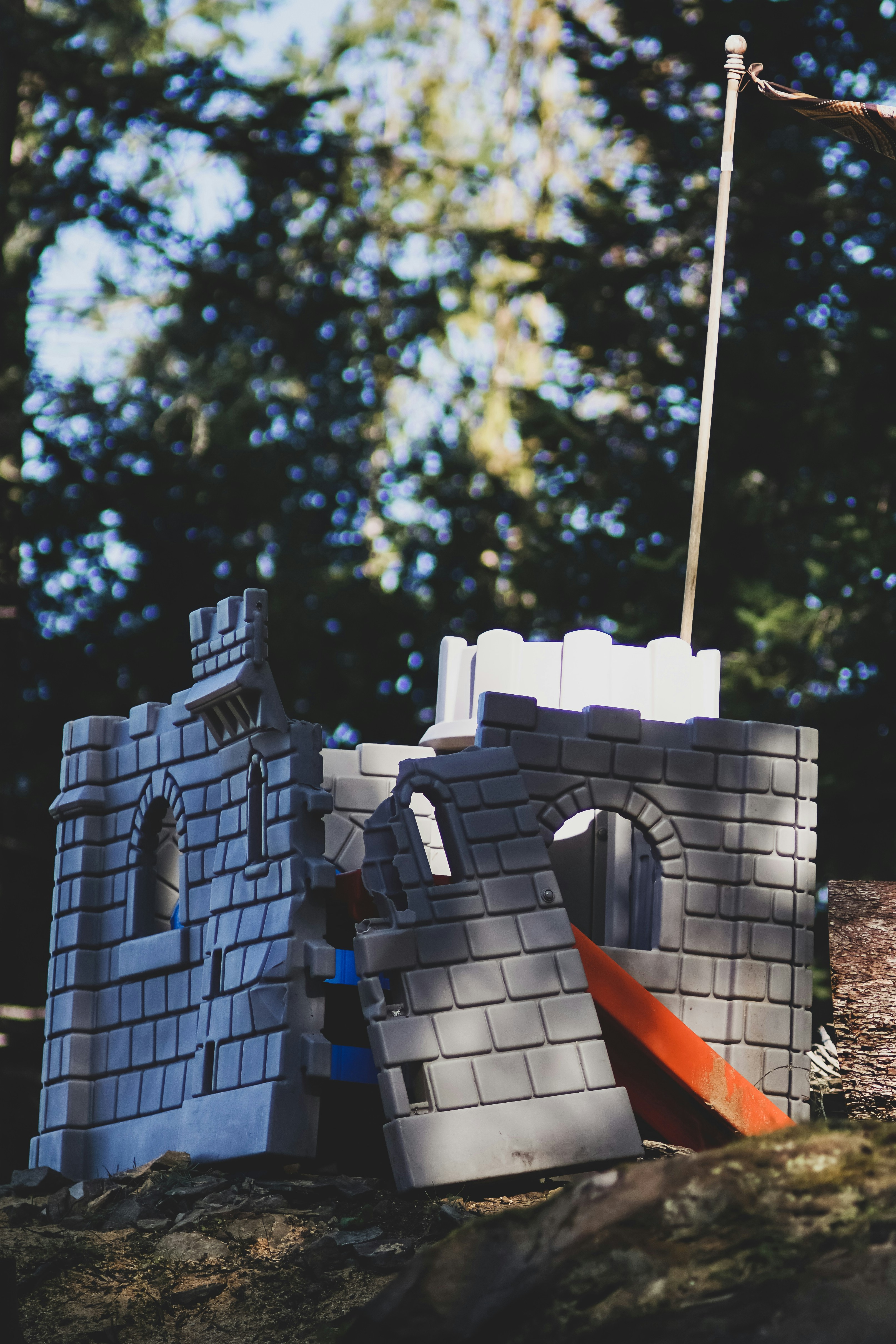 Colorful play castle with stone-like walls and a flag, nestled in a sunlit forest setting.