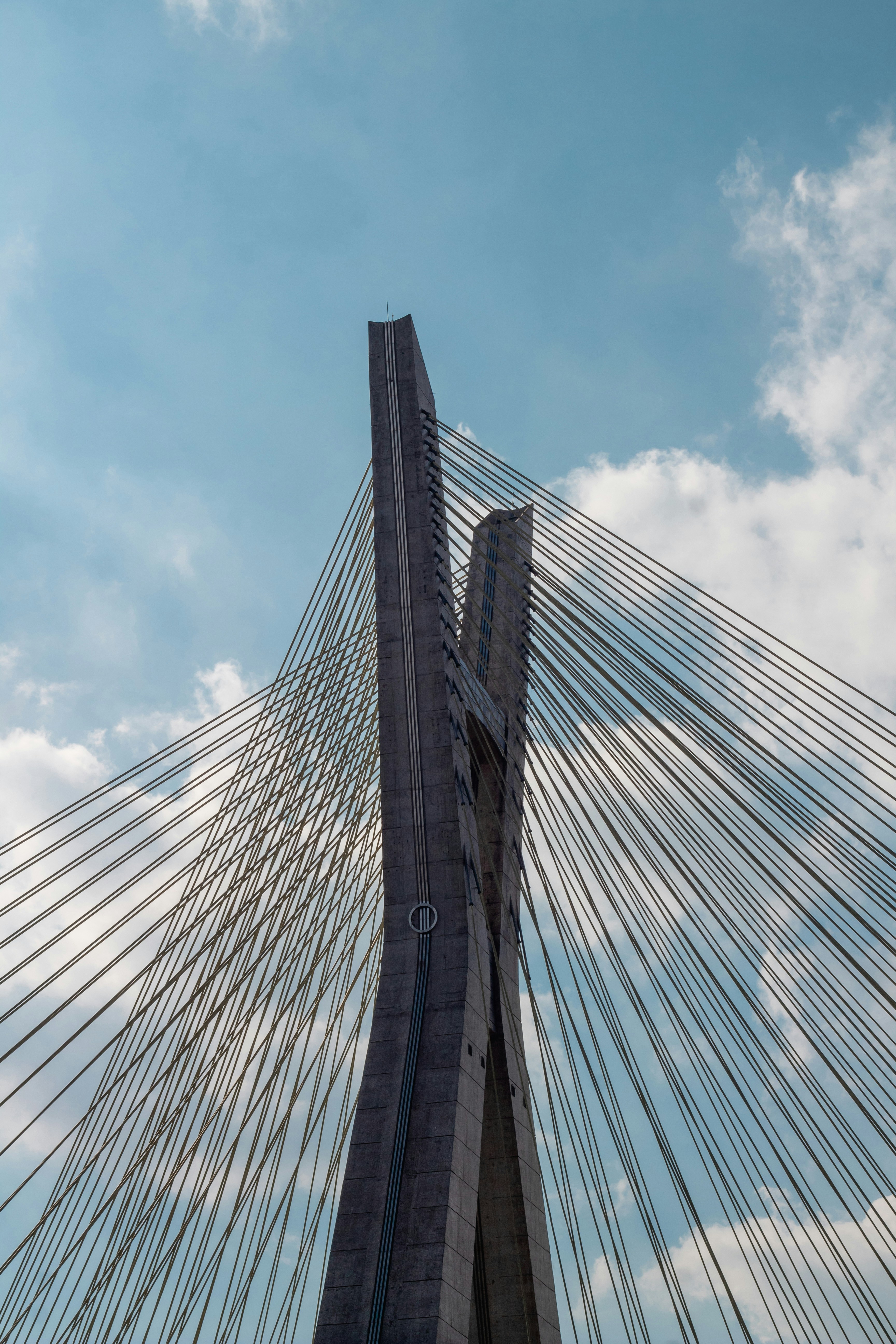A striking suspension bridge tower rising against a backdrop of blue sky and scattered clouds.