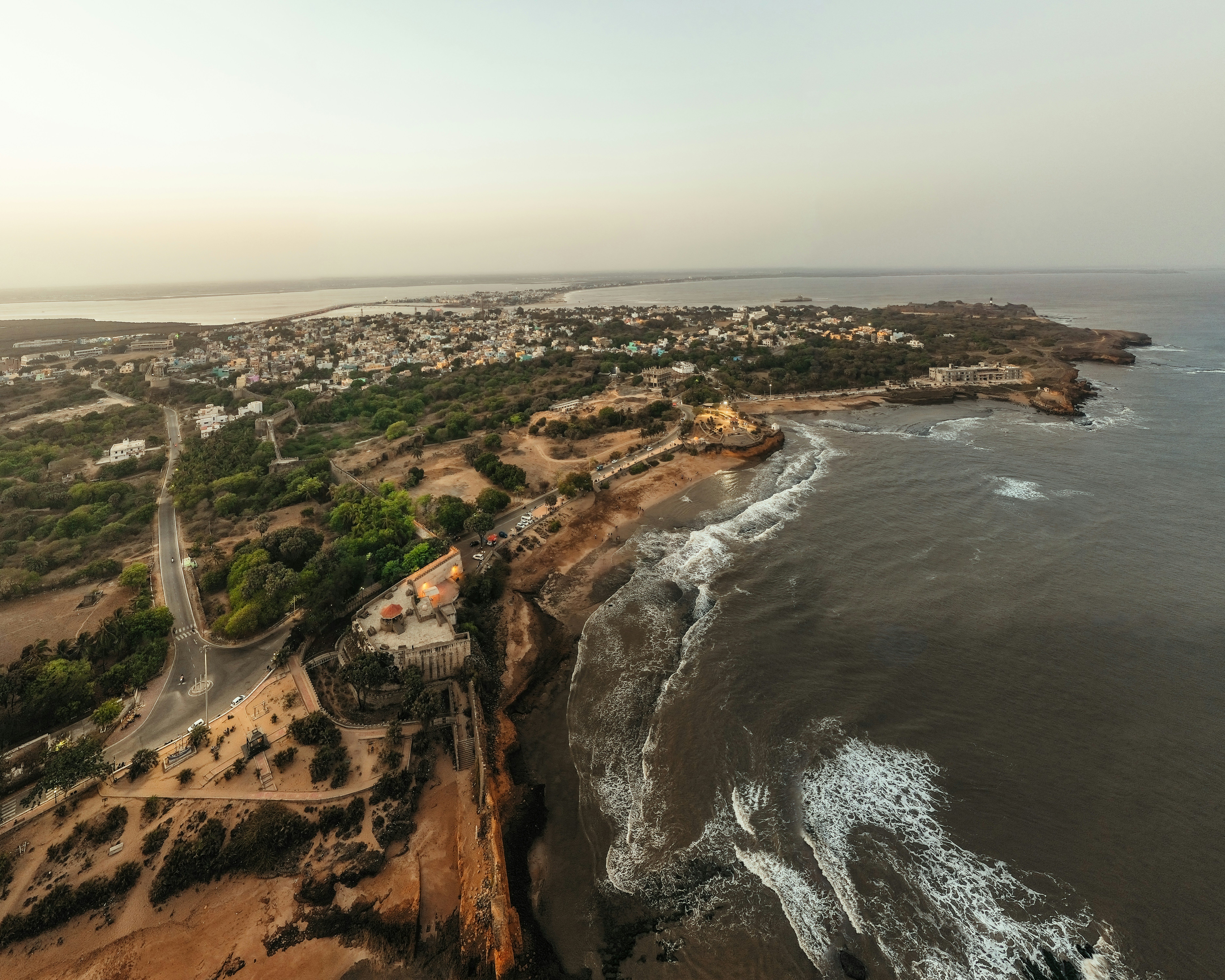 Aerial view of a coastal landscape, showcasing a blend of rugged cliffs, gentle waves, and a sprawling town nestled among greenery.
