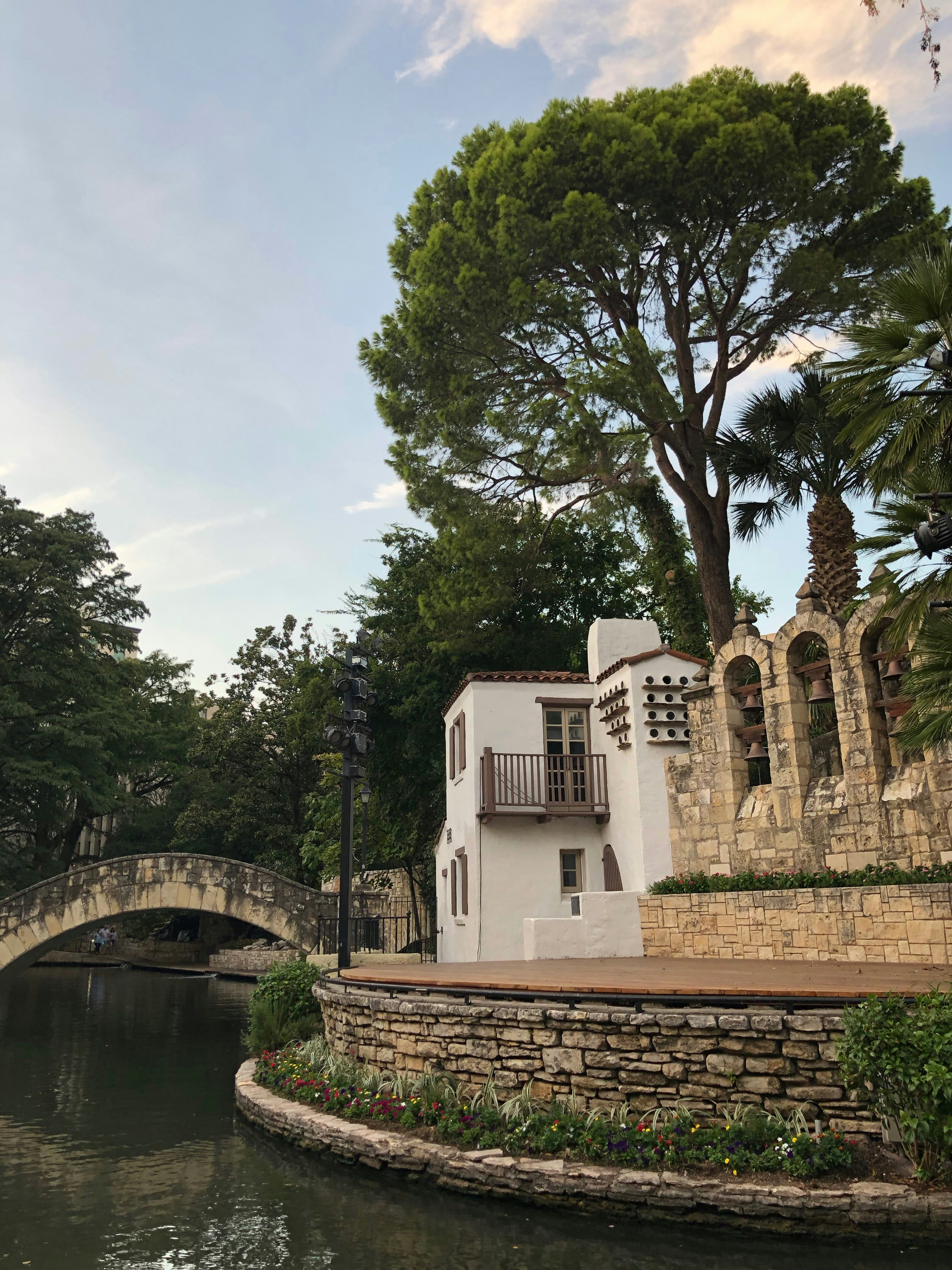 Waterfront stone terrace with arched bridge under towering trees