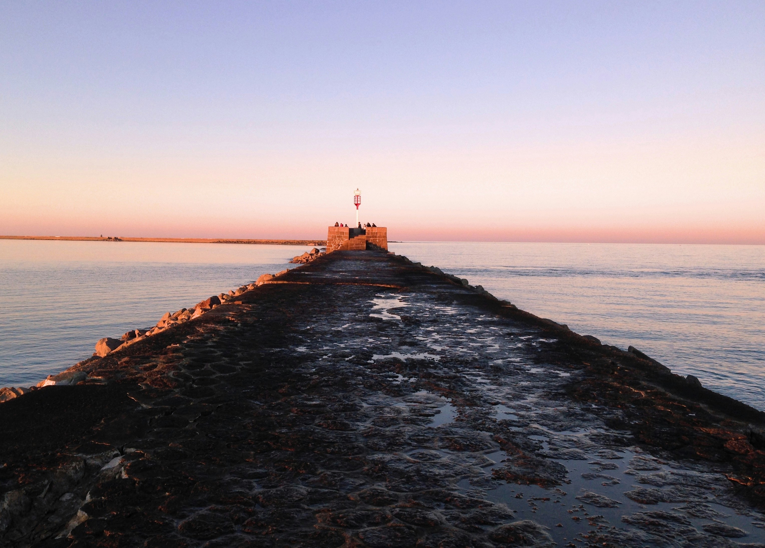 Long pier extending into calm waters at dusk with a soft pastel sky.