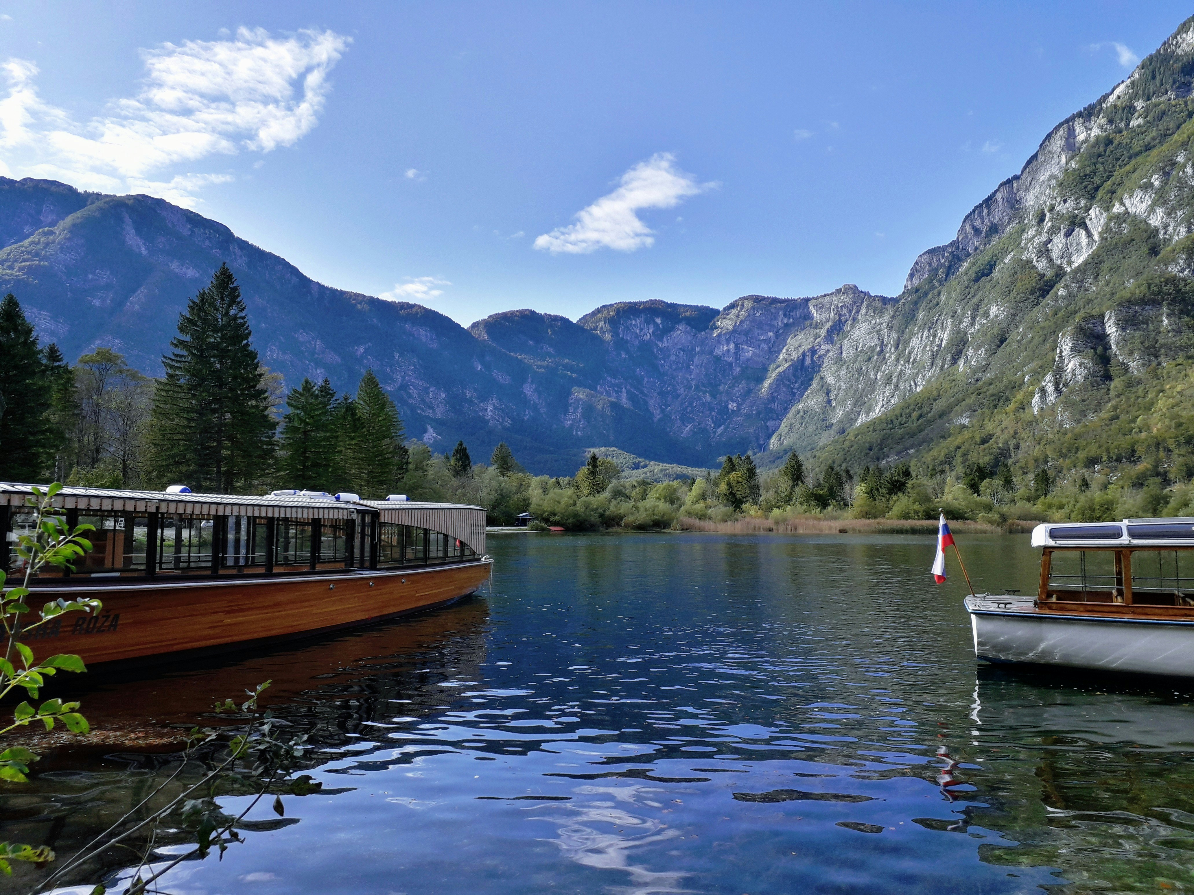 Two boats anchored on a tranquil lake, framed by towering mountains and lush greenery. The scene captures the essence of peaceful nature.