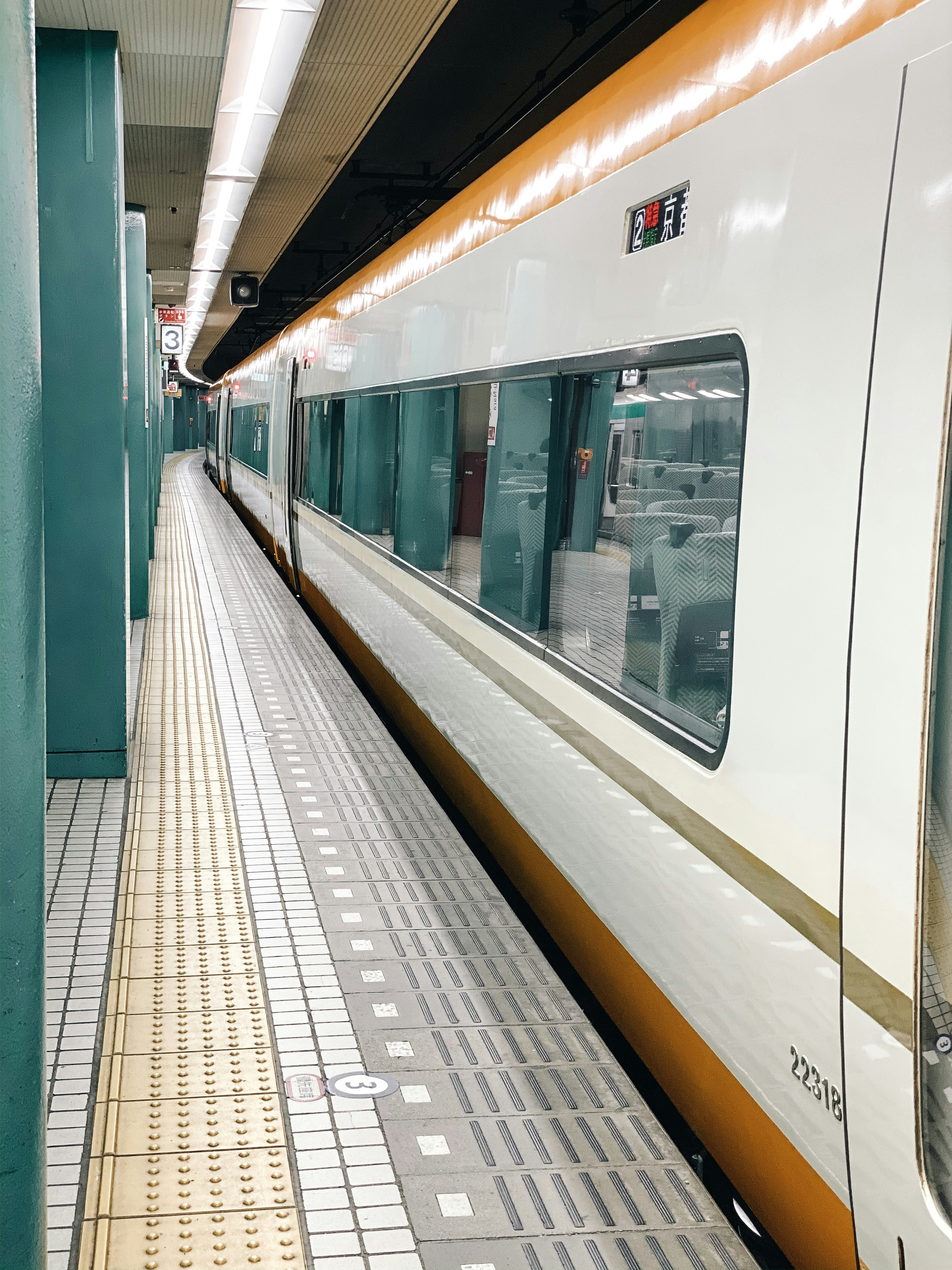 A sleek train awaits at a modern station, showcasing its streamlined design against a backdrop of vibrant green pillars and tiled flooring.