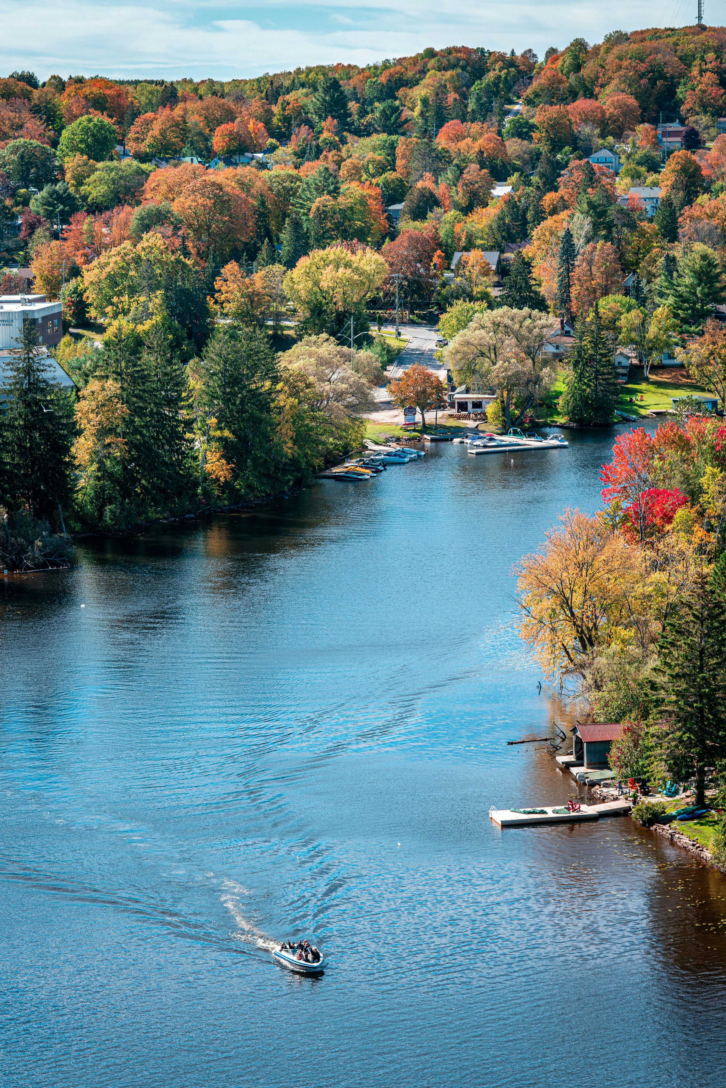Speedboat cruising along a tree-lined river amidst vibrant fall foliage.