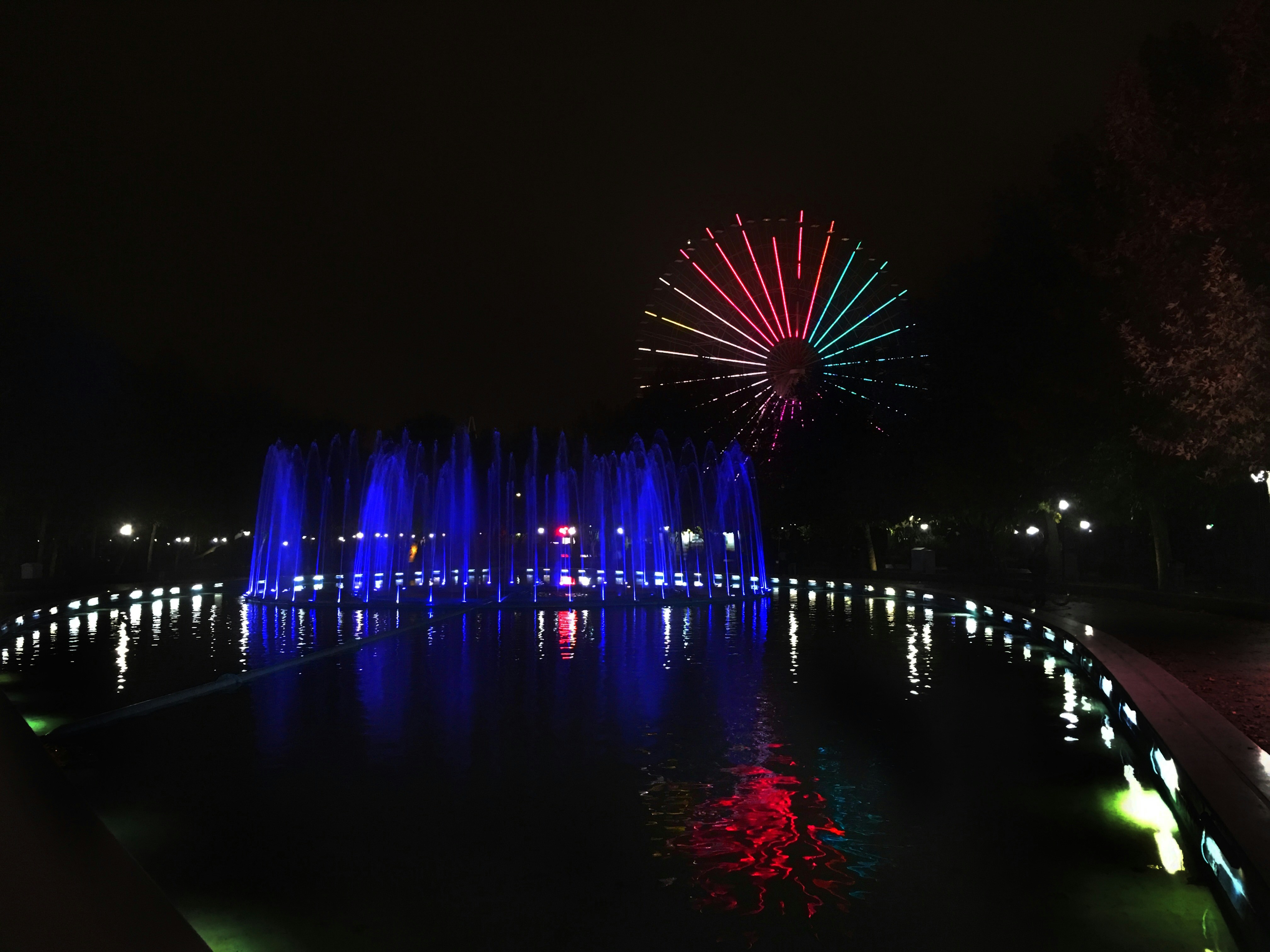 Neon Cascade Over Water: A Blue Fountain Meets the Ferris Wheel