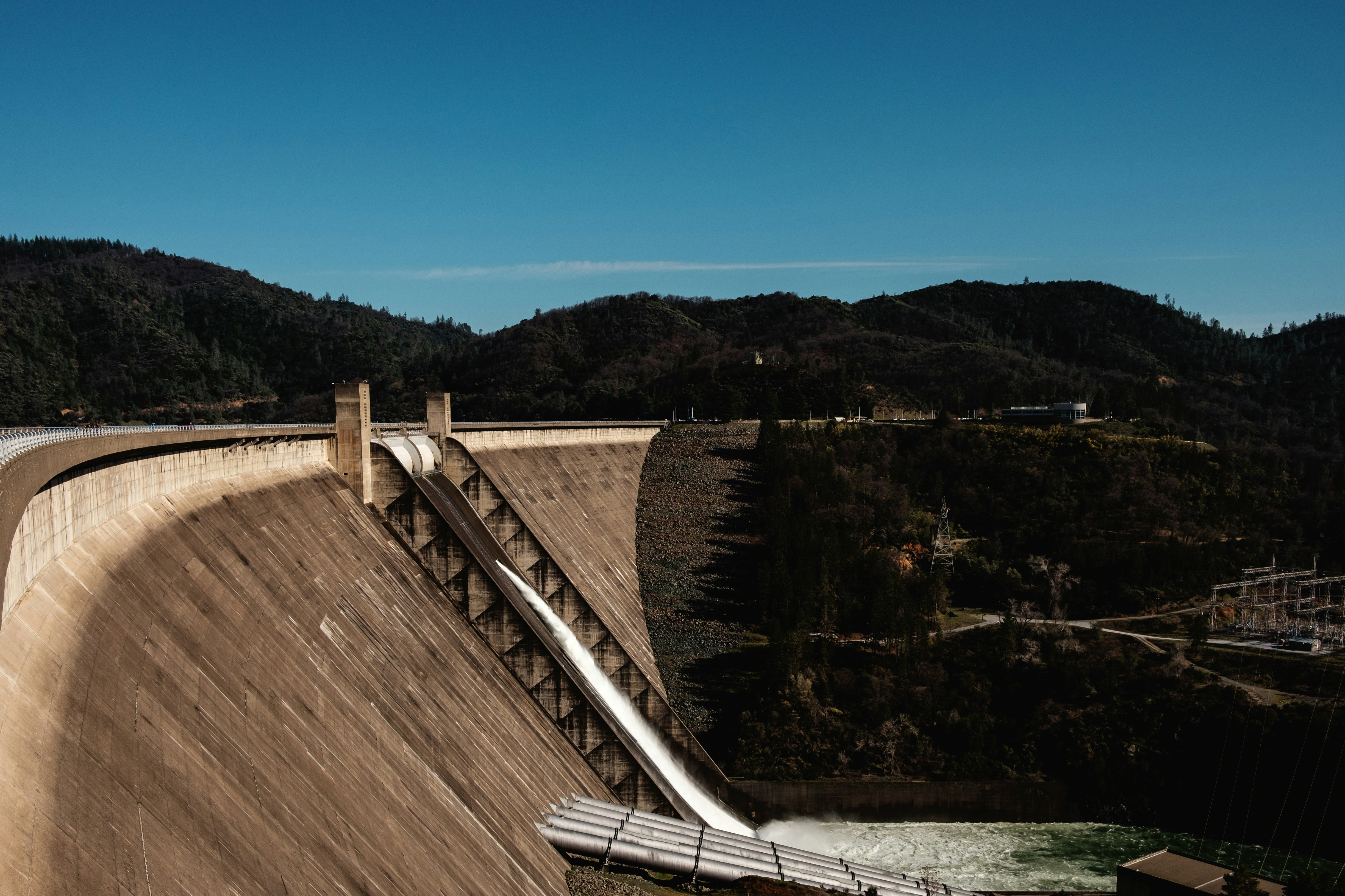 Concrete dam against a backdrop of rolling hills under a clear blue sky.
