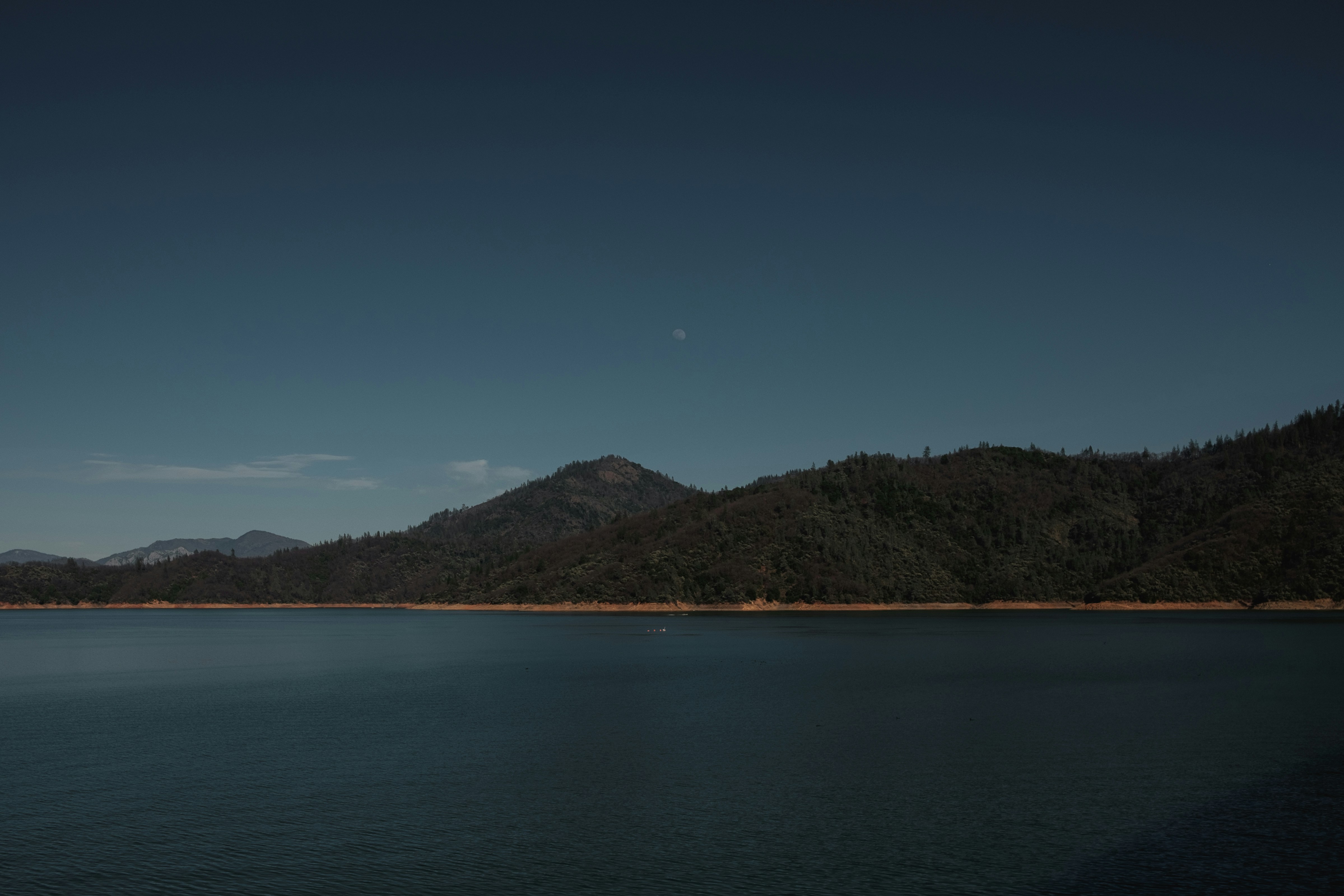 Calm lake reflecting distant mountains under a clear blue sky, showcasing nature's tranquility.