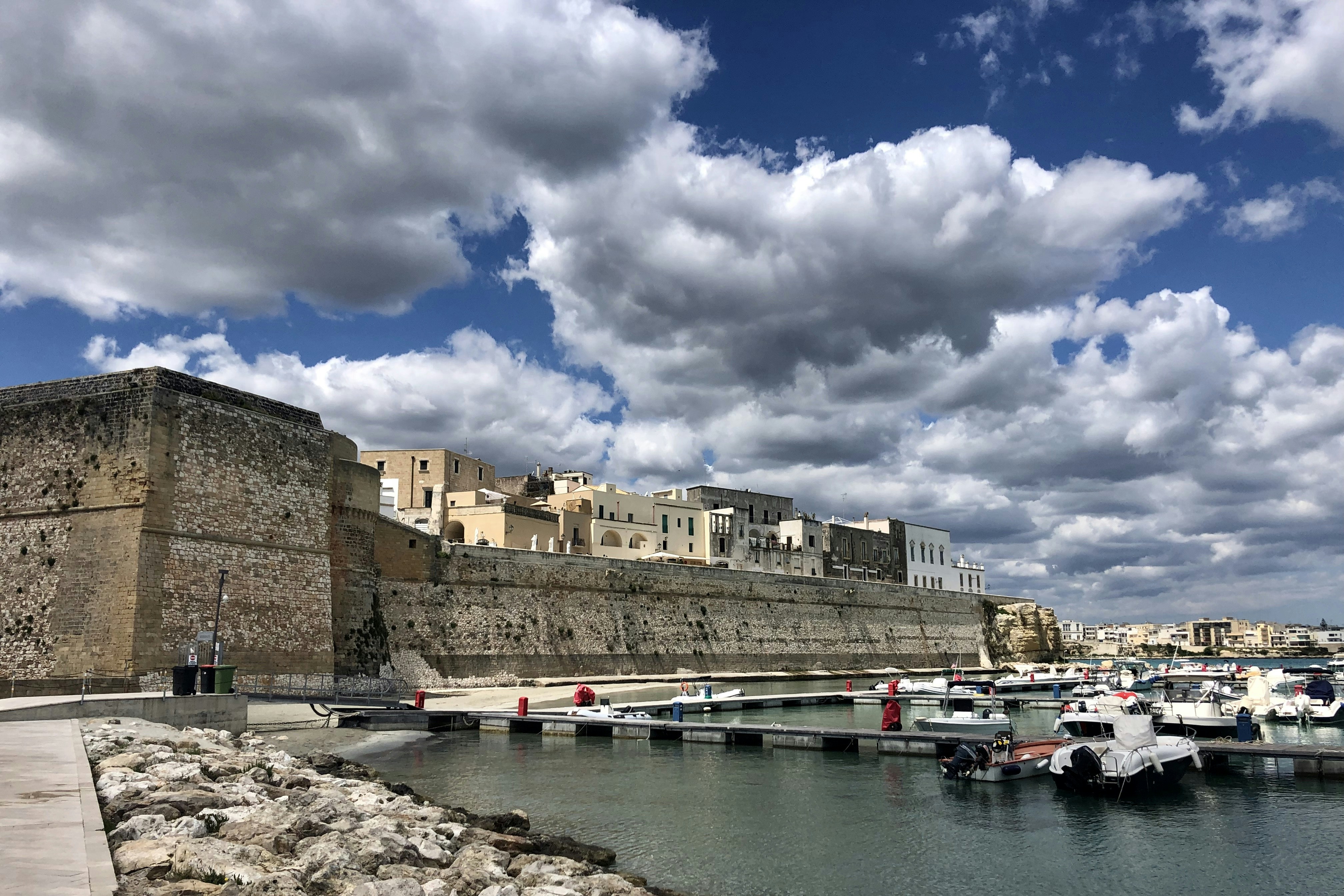 Clouds gather above a fortified harbor with boats moored along the pier.