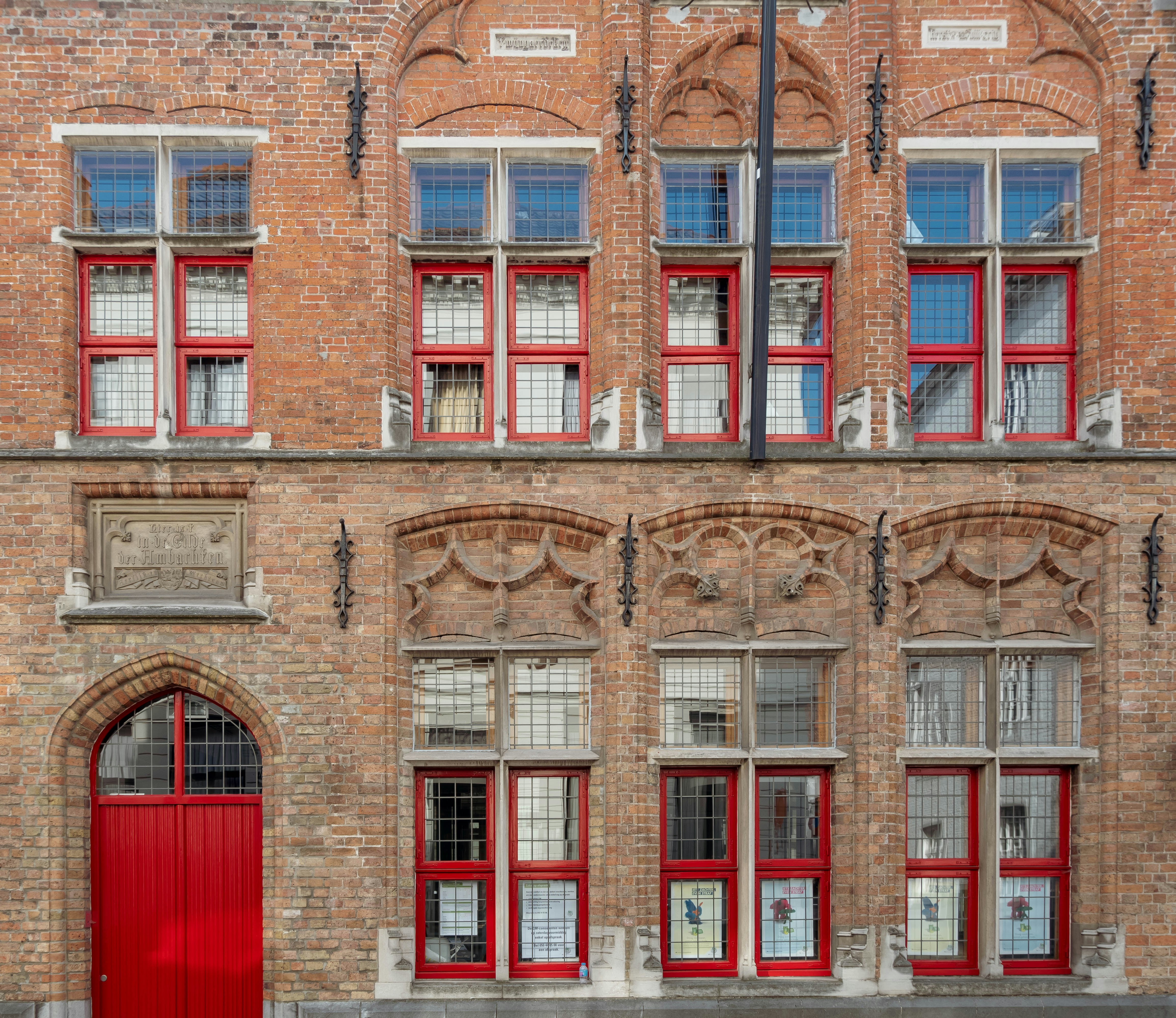 Historic brick building featuring intricate architectural details and vibrant red window frames and door. A showcase of classic design elements.