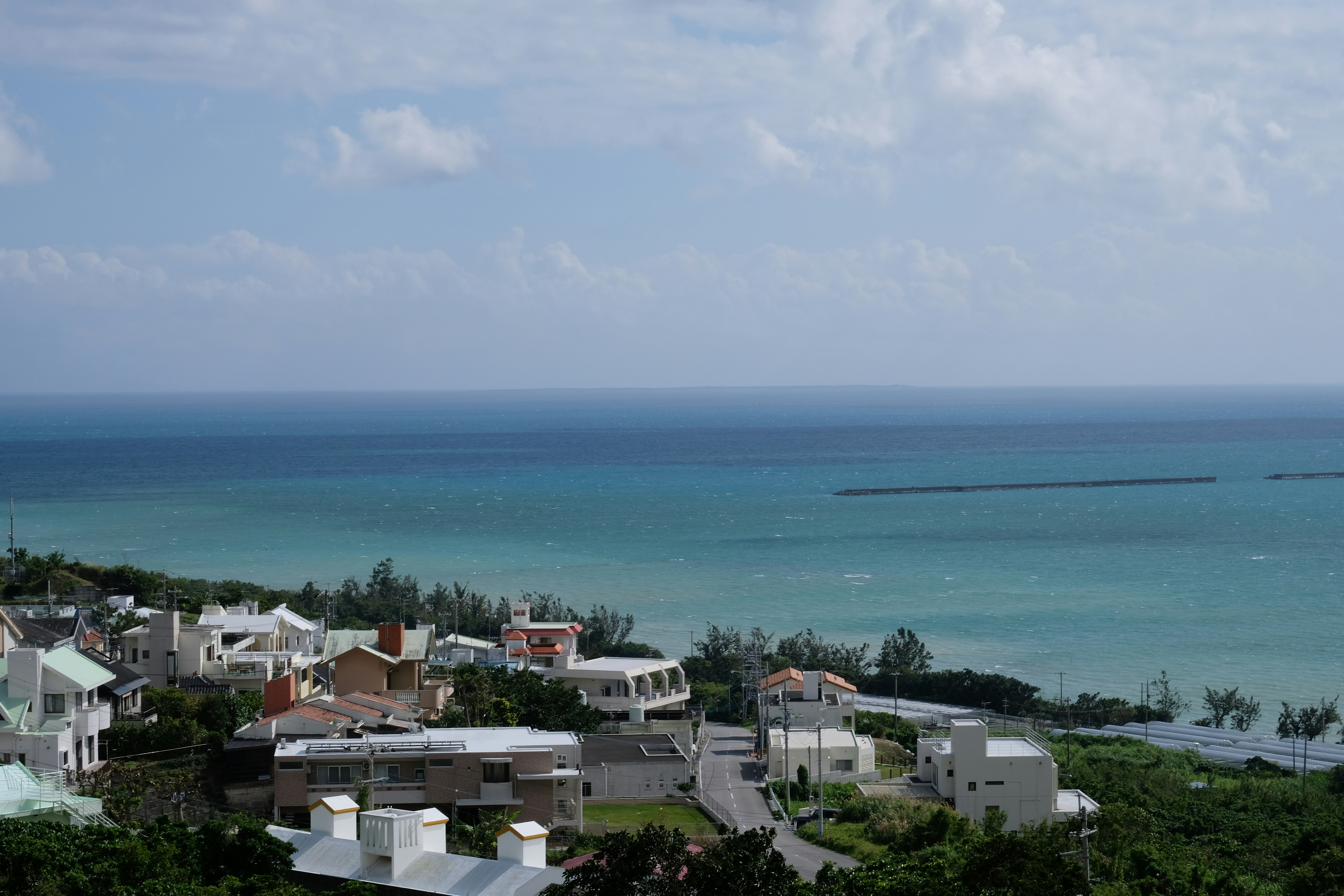 A vibrant coastal view showcasing a blend of residential architecture and the expansive ocean, with gentle waves lapping against the shore. 
