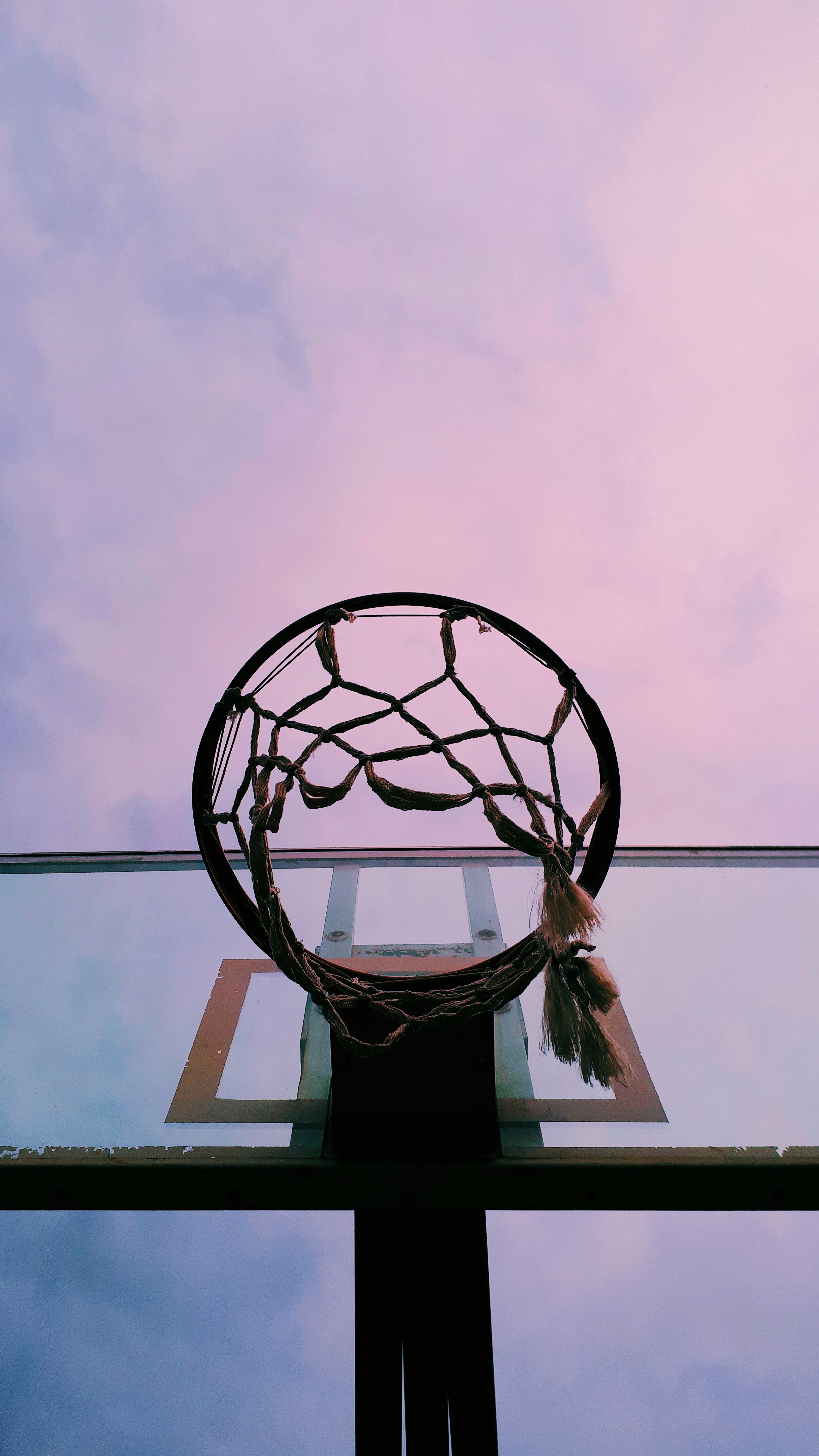 Basketball hoop framed against a pastel sky, showcasing the net's intricate details and the glass backboard's reflection.