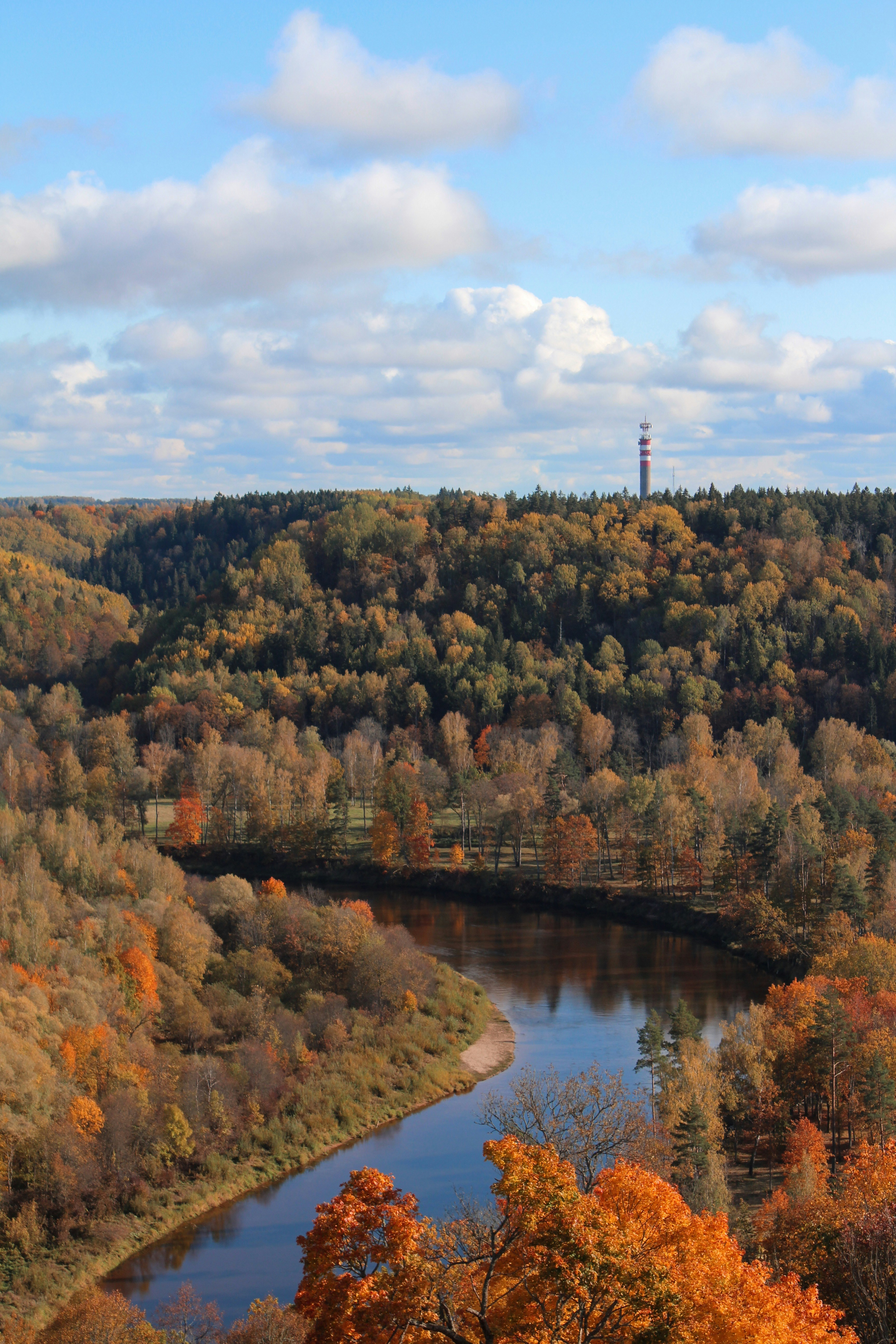 A winding river flows through a vibrant autumn landscape, framed by colorful foliage and distant hills under a partly cloudy sky.