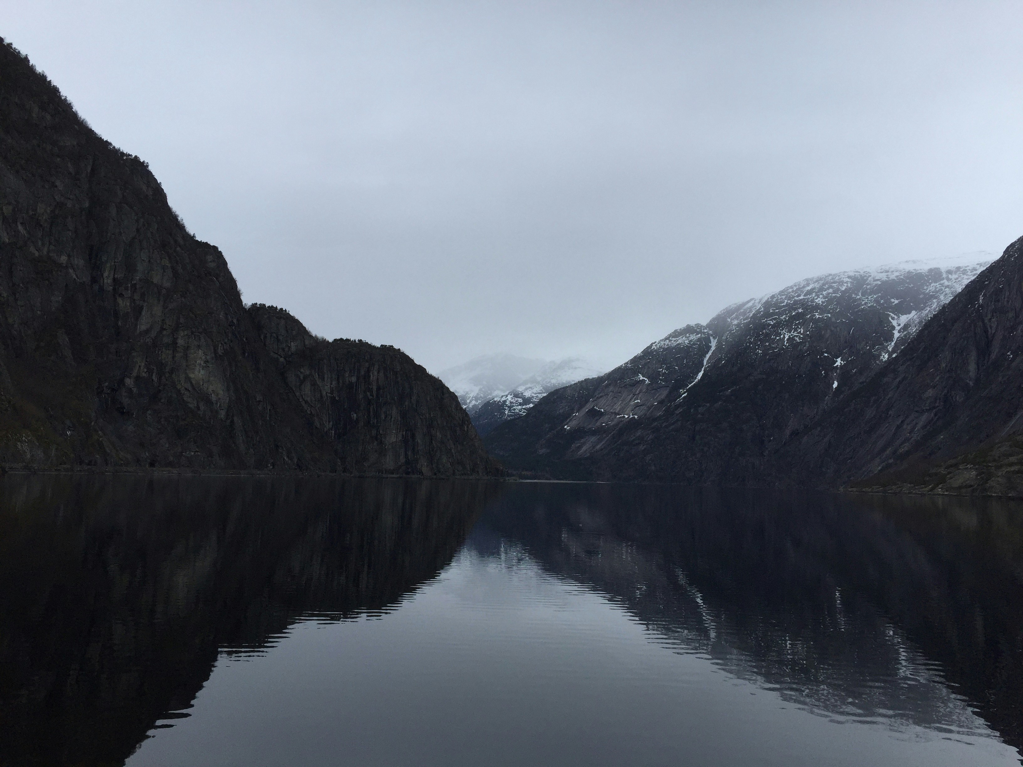 A tranquil fjord scene with towering mountains reflecting on still waters under a cloudy sky.