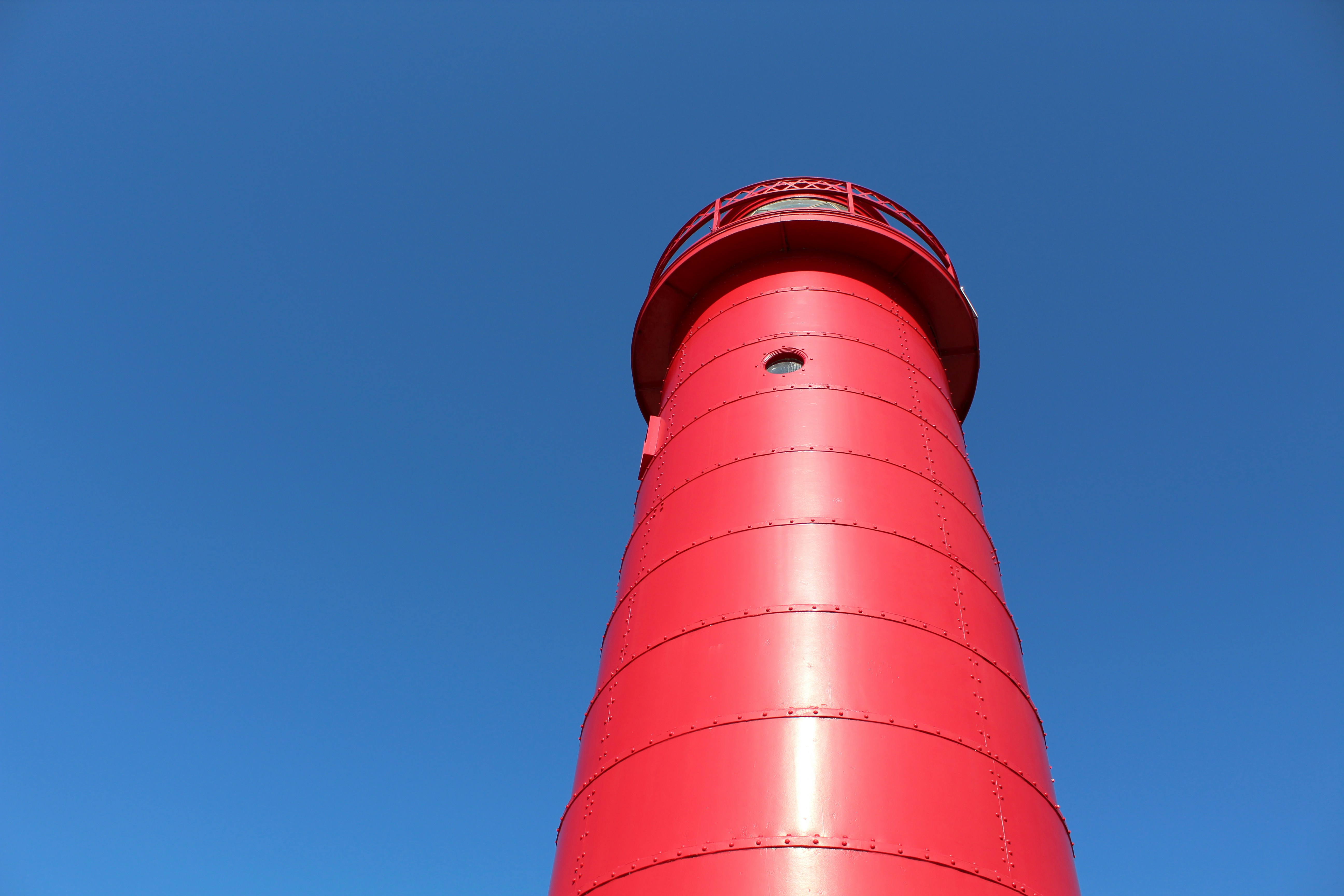 Crimson Beacon Under a Sapphire Sky: A Low-Angle Portrait of a Red Lighthouse