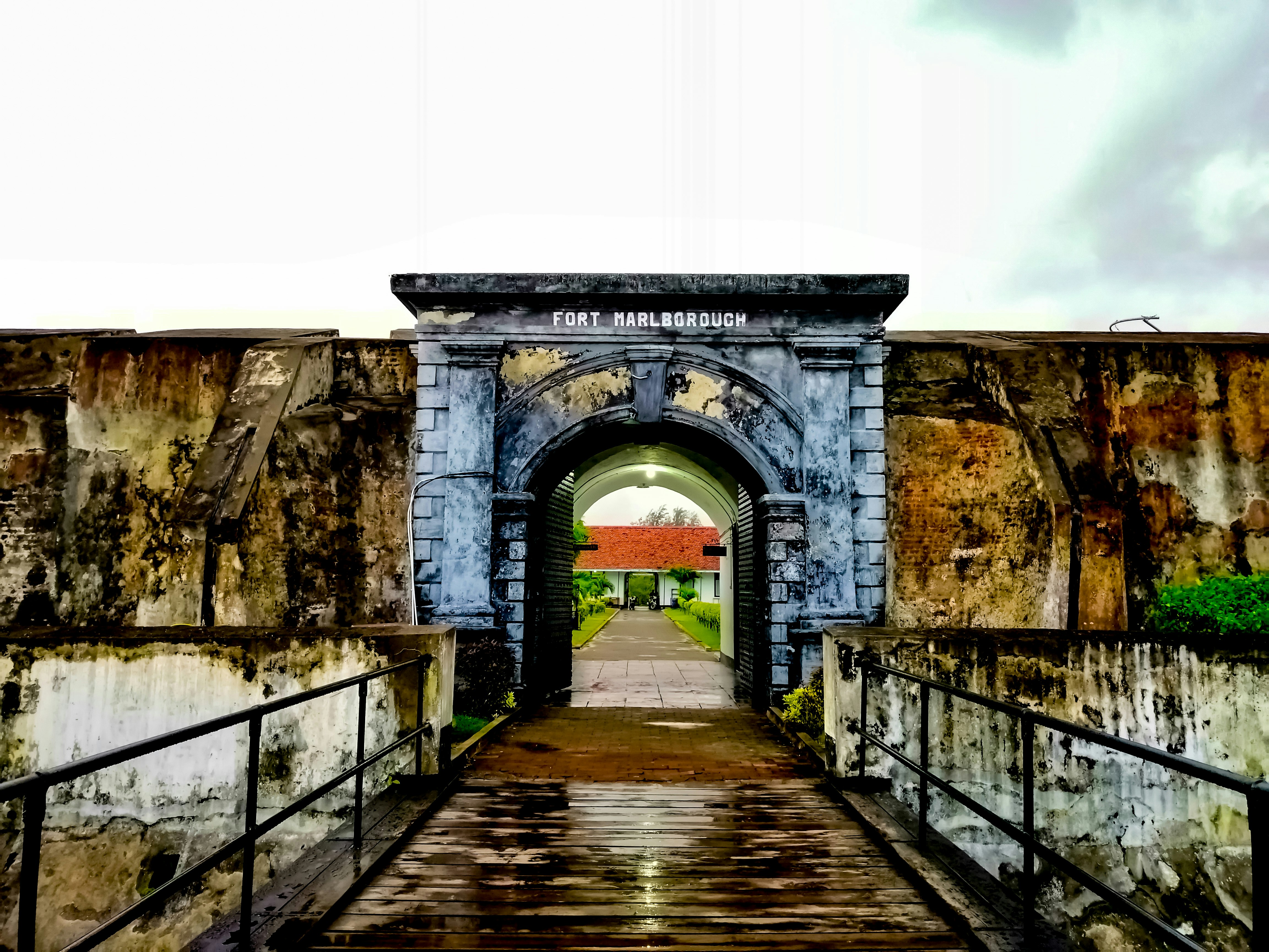 Weathered stone archway leading into a historic fort, with wet ground reflecting overcast sky.